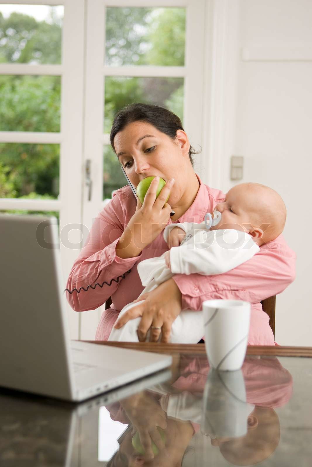A multitasking mother who works at home while taking care of her baby ...