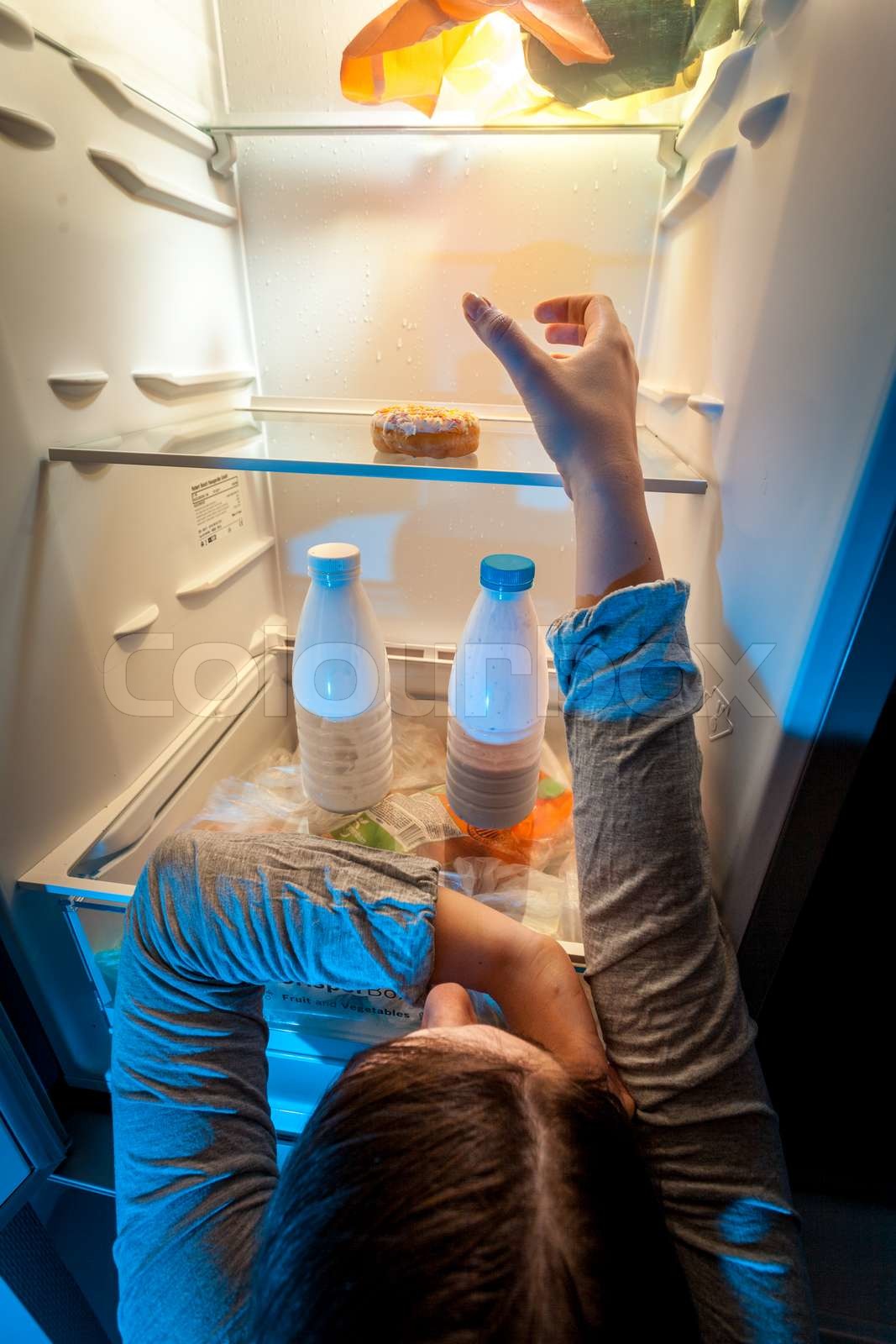 woman taking donut from top shelf of refrigerator | Stock image | Colourbox