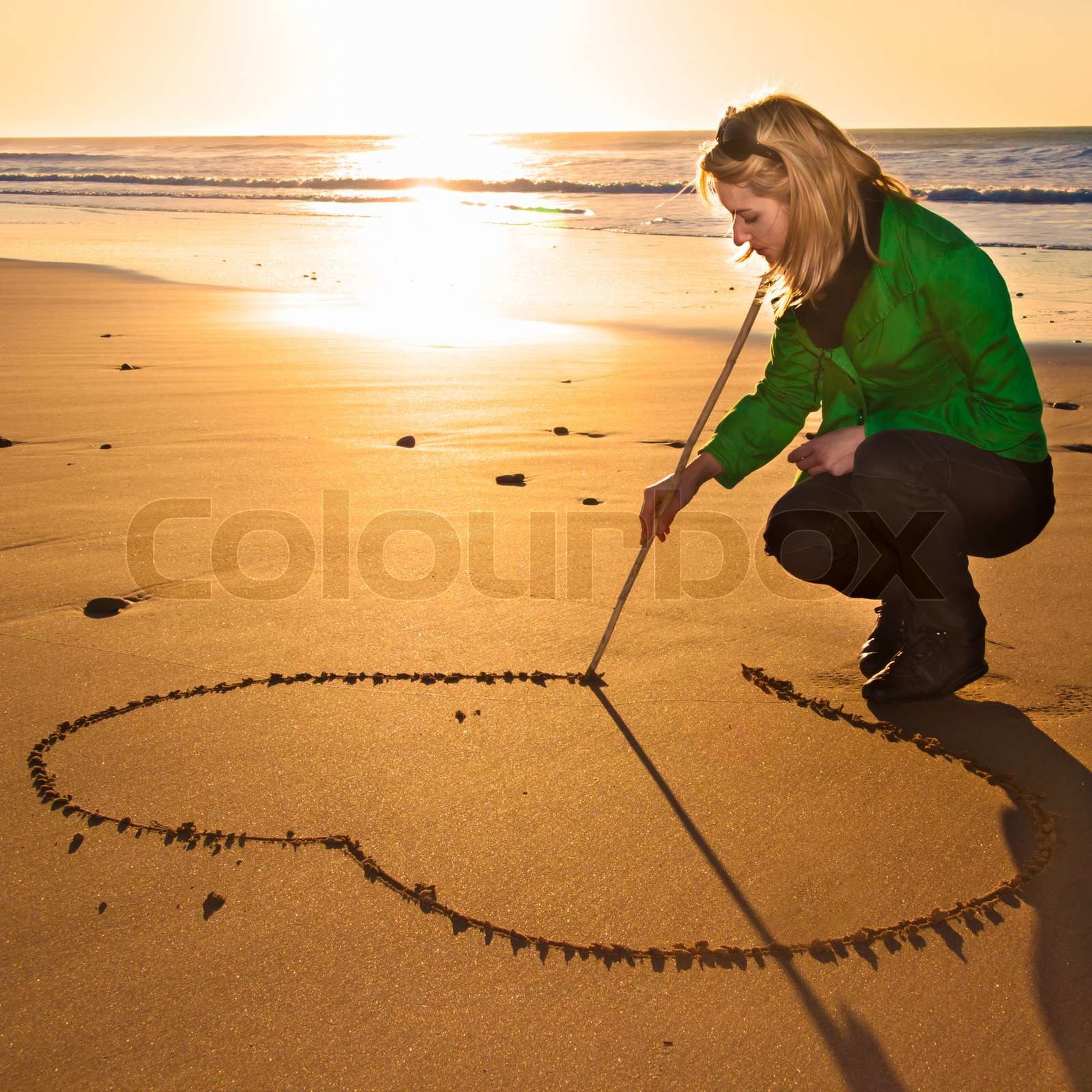 Woman drowing a heart shape in the sand. | Stock image | Colourbox