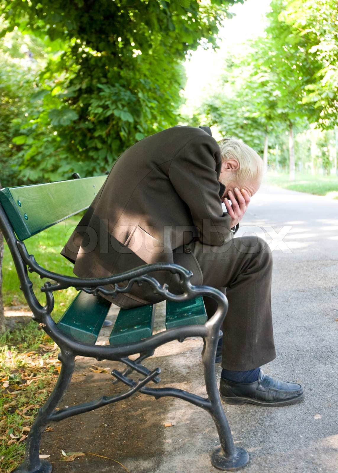 A sad elderly man sitting on a park bench | Stock image | Colourbox
