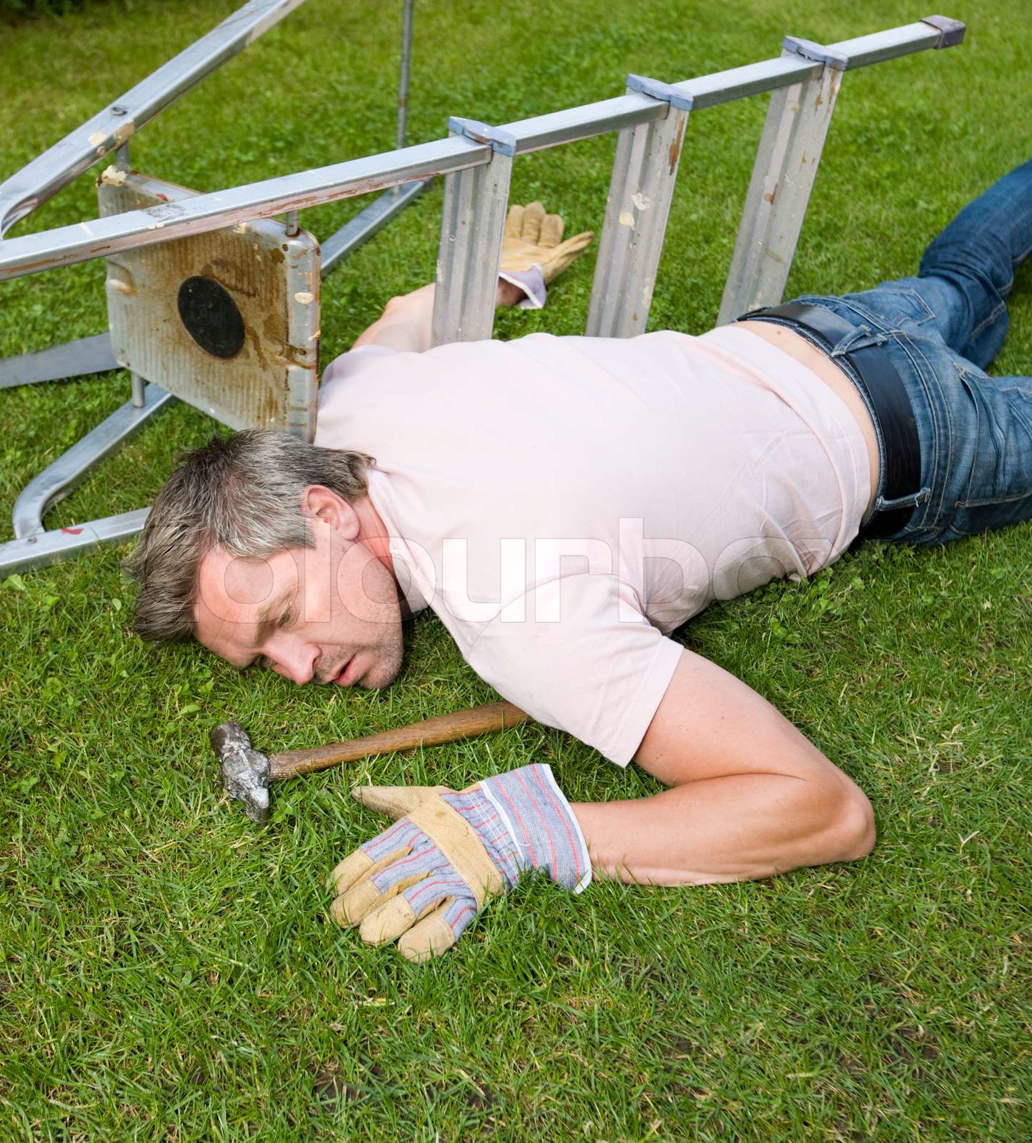 A man lies on a grass lawn after falling from a ladder | Stock image ...