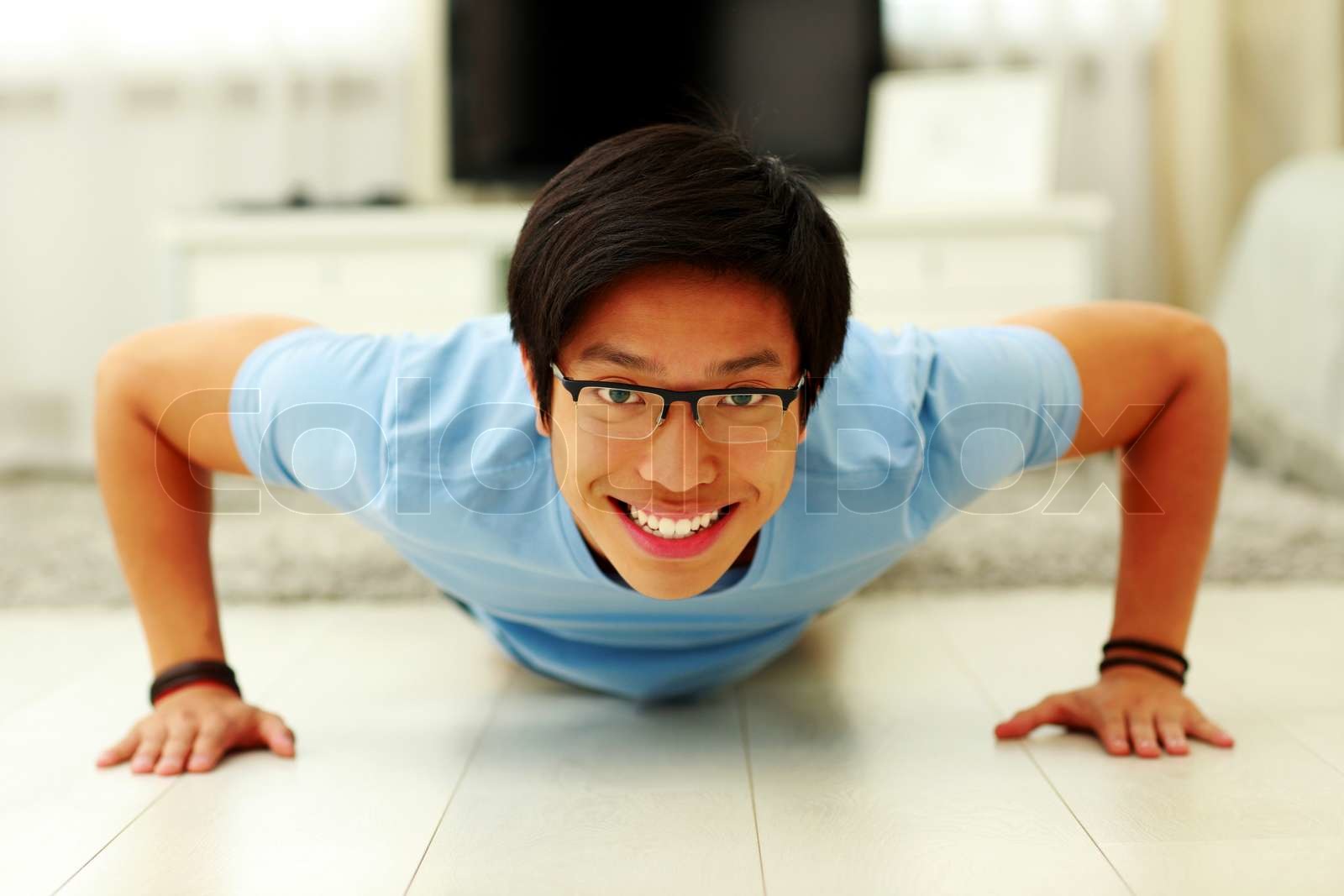 Portrait of a happy young man doing push ups in the living room at home ...