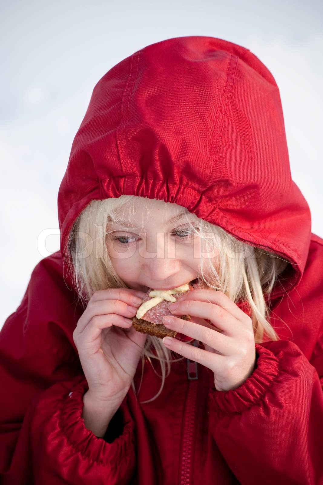 Nærbillede af en blond pige i en rød jakke der spiser udendørs | Stock ...