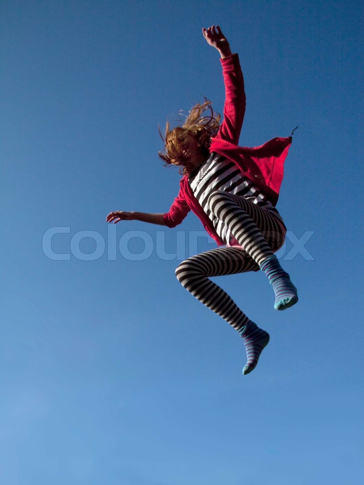 Little girl jumping high in the air with blue sky | Stock image | Colourbox
