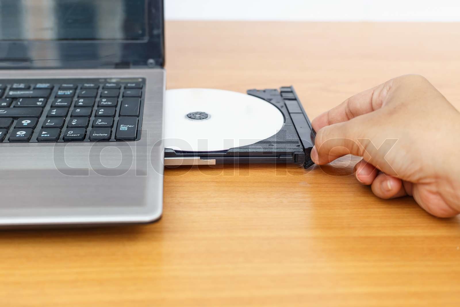 Hand inserting a cd on laptop on table | Stock image | Colourbox
