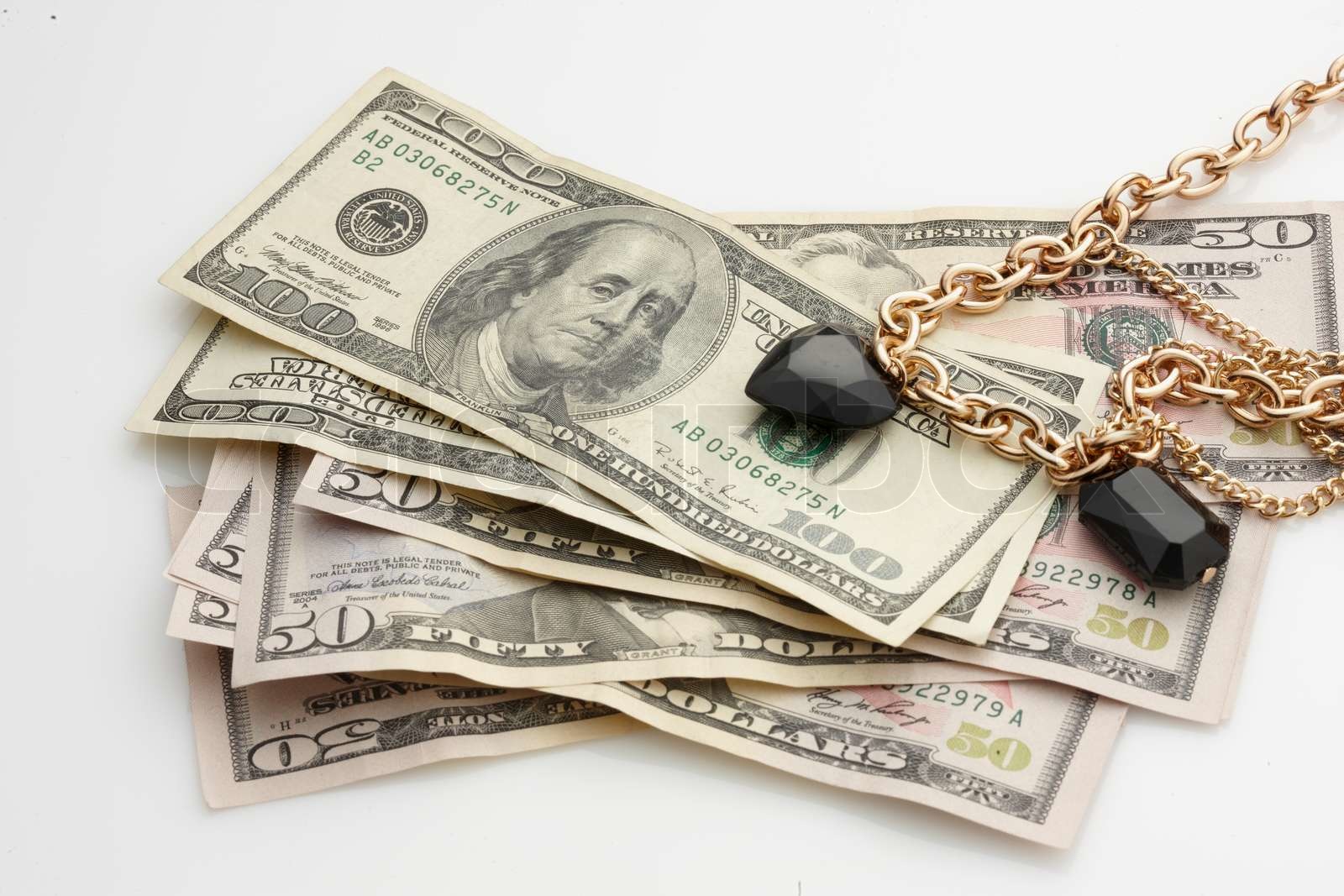 A stack of American dollar bills and gold chain necklace with a black ...