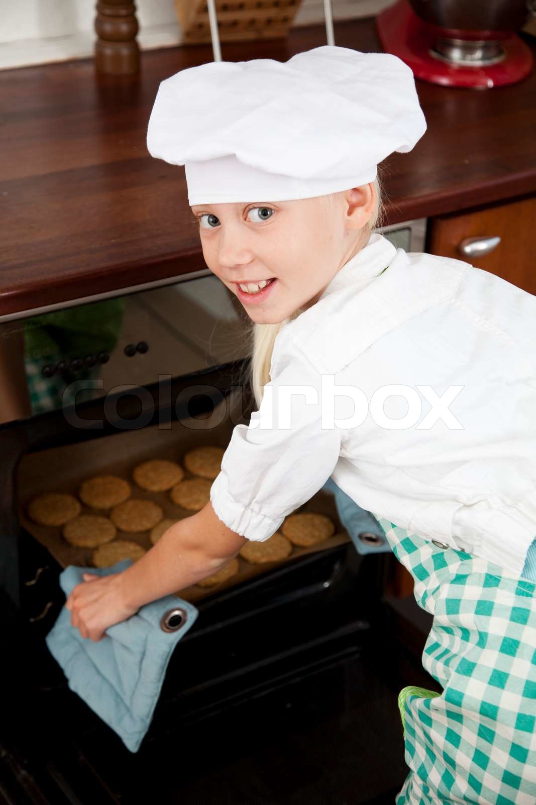 A young baker getting freshly baked cookies from the over | Stock image ...