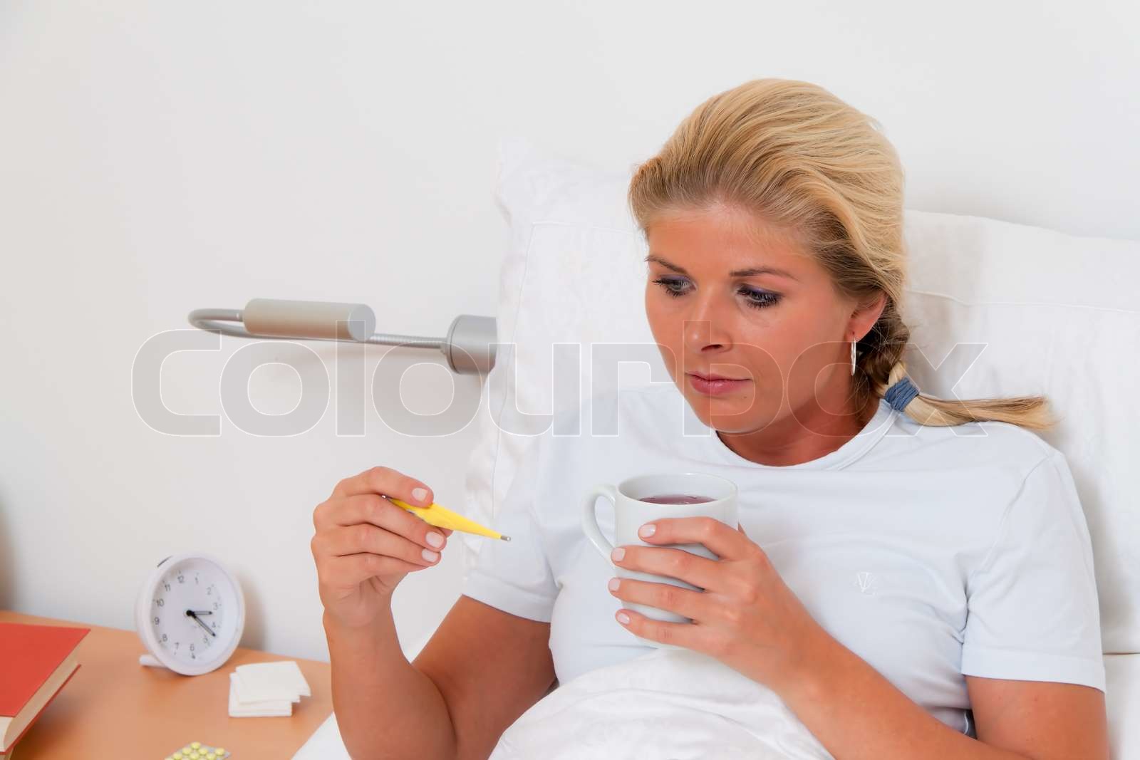 eine Frau liegt krank im Bett und hat ein Fieberthermometer. | Stock ...