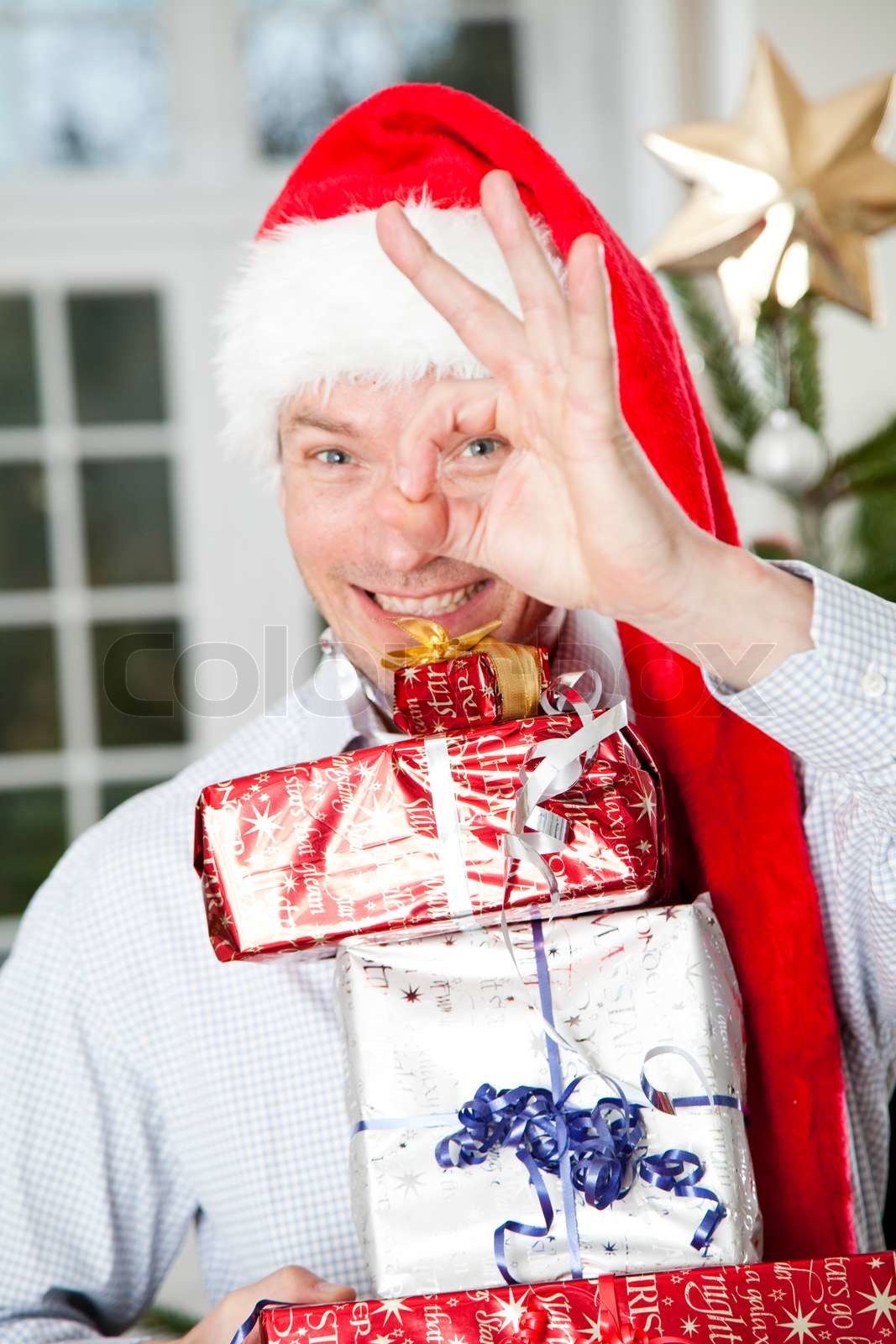 En mand med nissehue på og gaver står foran juletræet | Stock foto ...