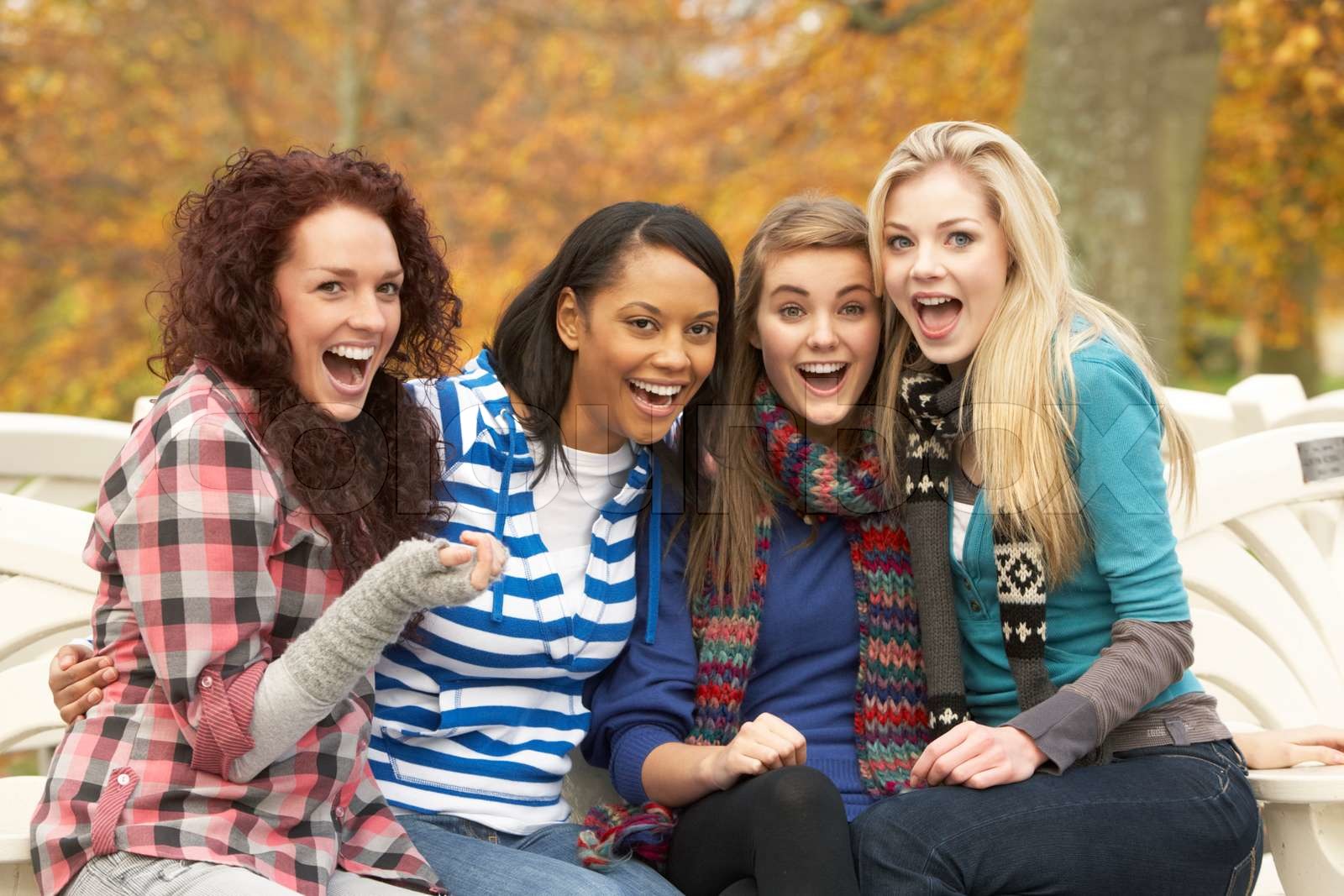 Group Of Four Teenage Girls Sitting On Bench In Autumn Park | Stock ...