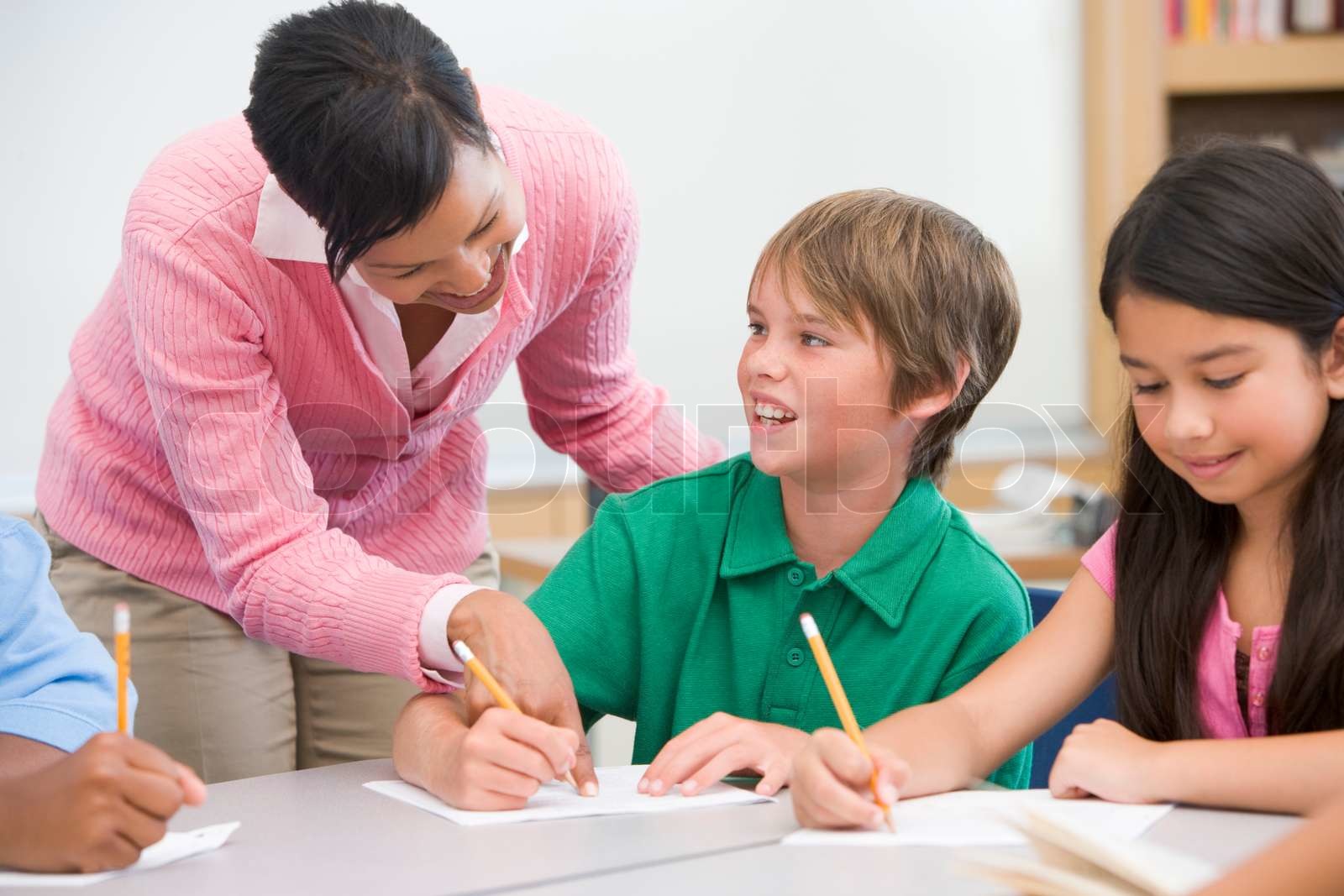 Lærer og elev i folkeskolen klasseværelse arbejder på skriftlige ...