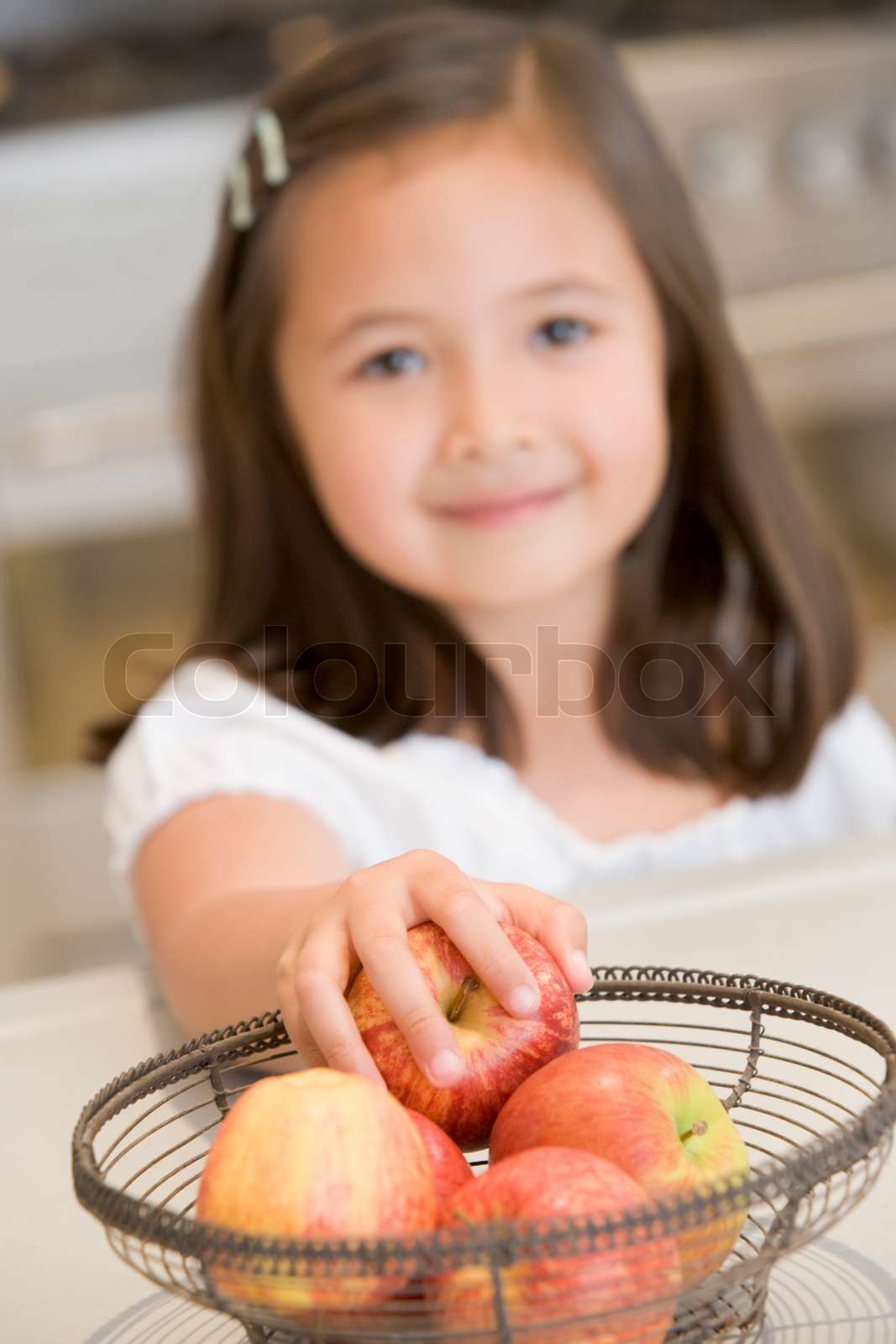 Girl taking apple from fruit basket at home | Stock image | Colourbox
