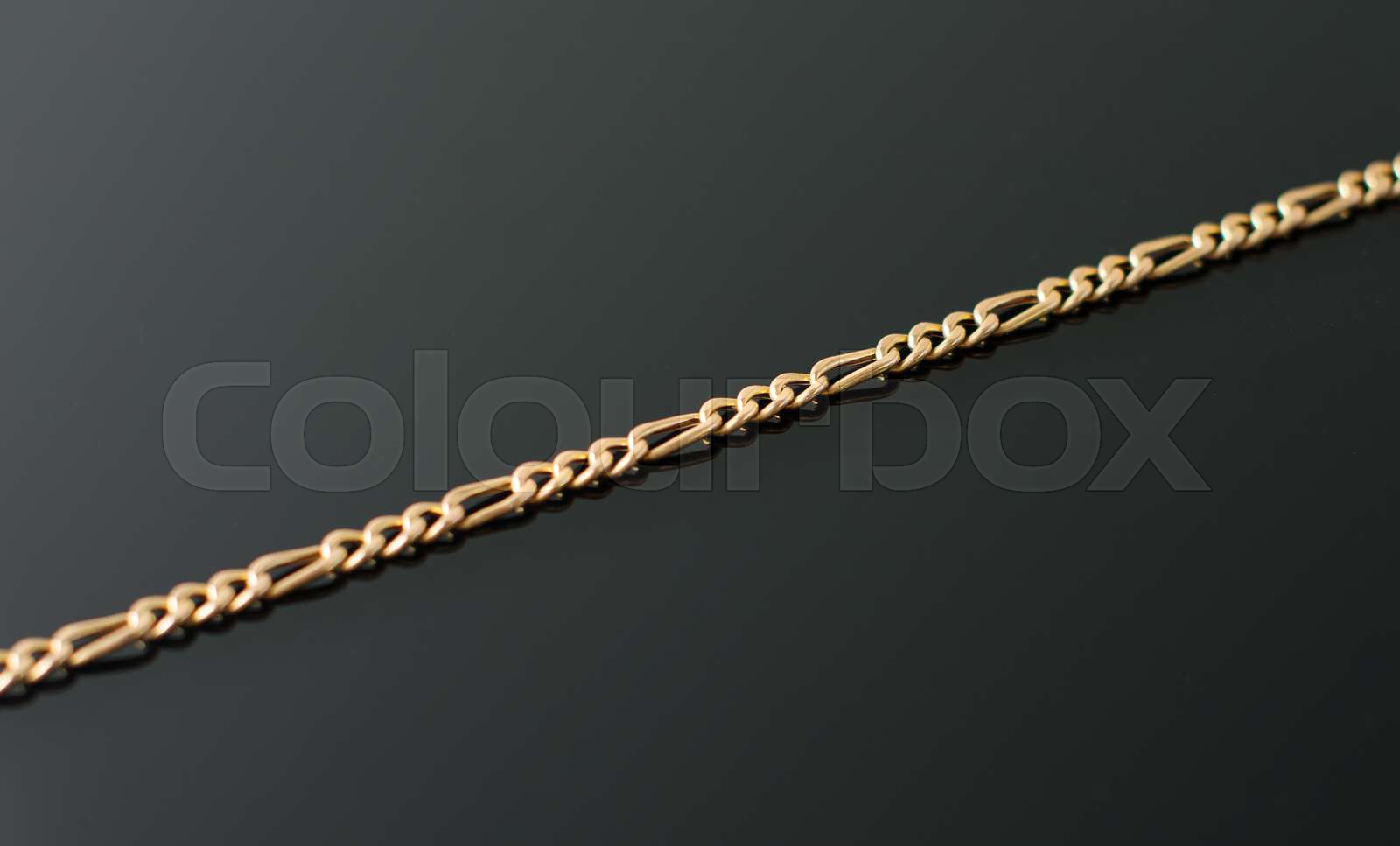 Gold chain lying on black table. | Stock image | Colourbox