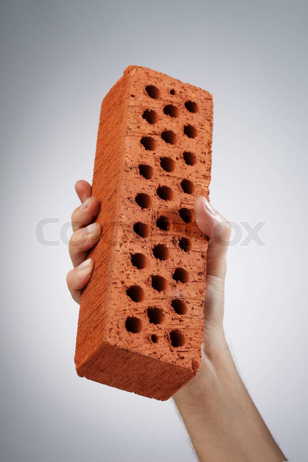 A hand holding a red perforated brick | Stock image | Colourbox