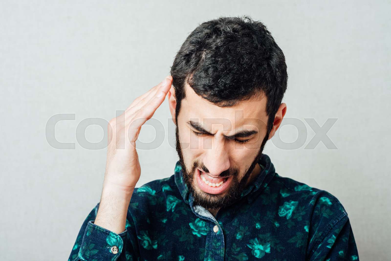 Man rubbing his throbbing forehead with his hand as he grimaces and ...