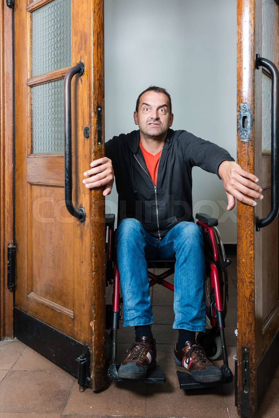 Man in wheelchair stuck between swing doors | Stock image | Colourbox