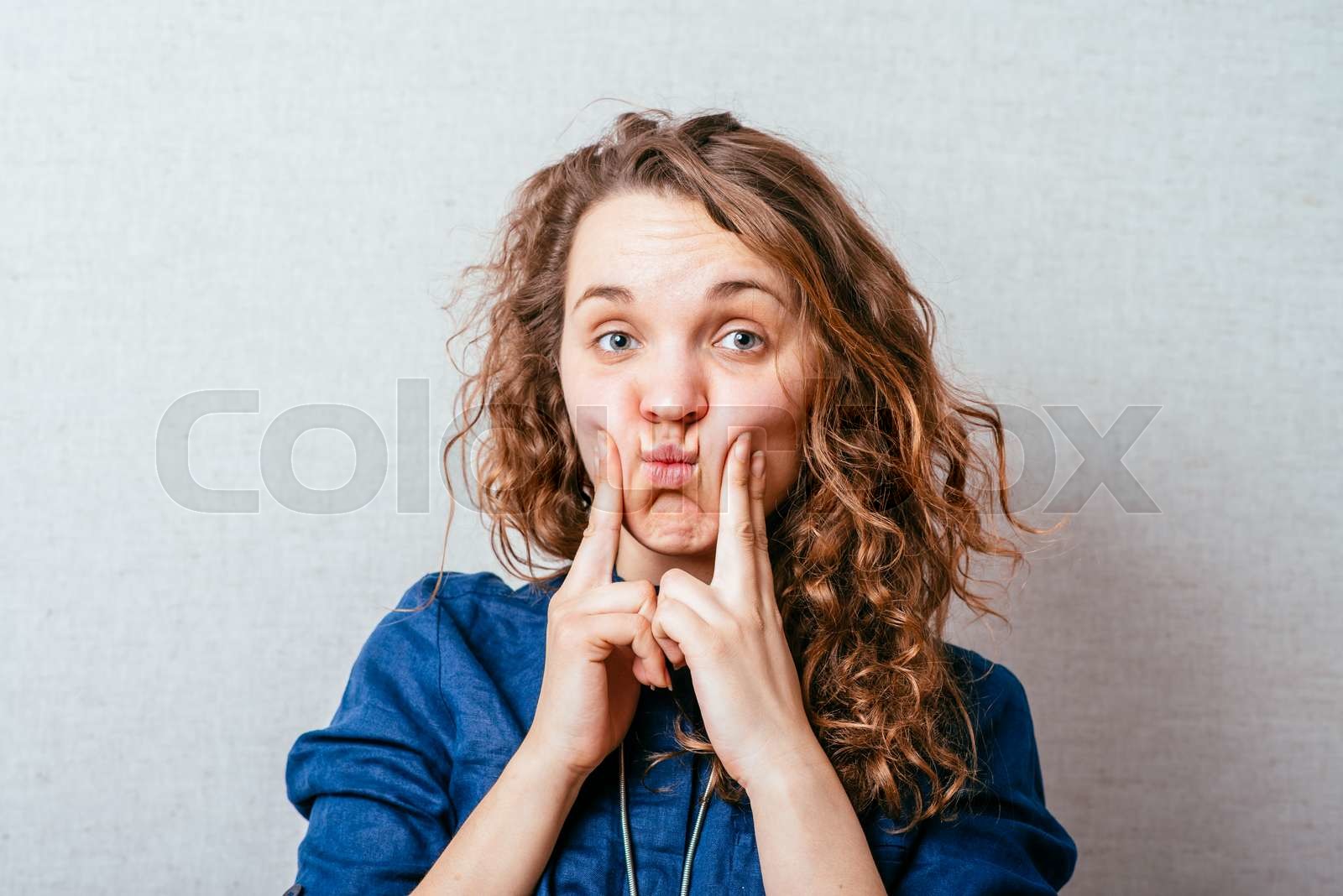 Young woman squeezing her cheeks with her hands | Stock image | Colourbox
