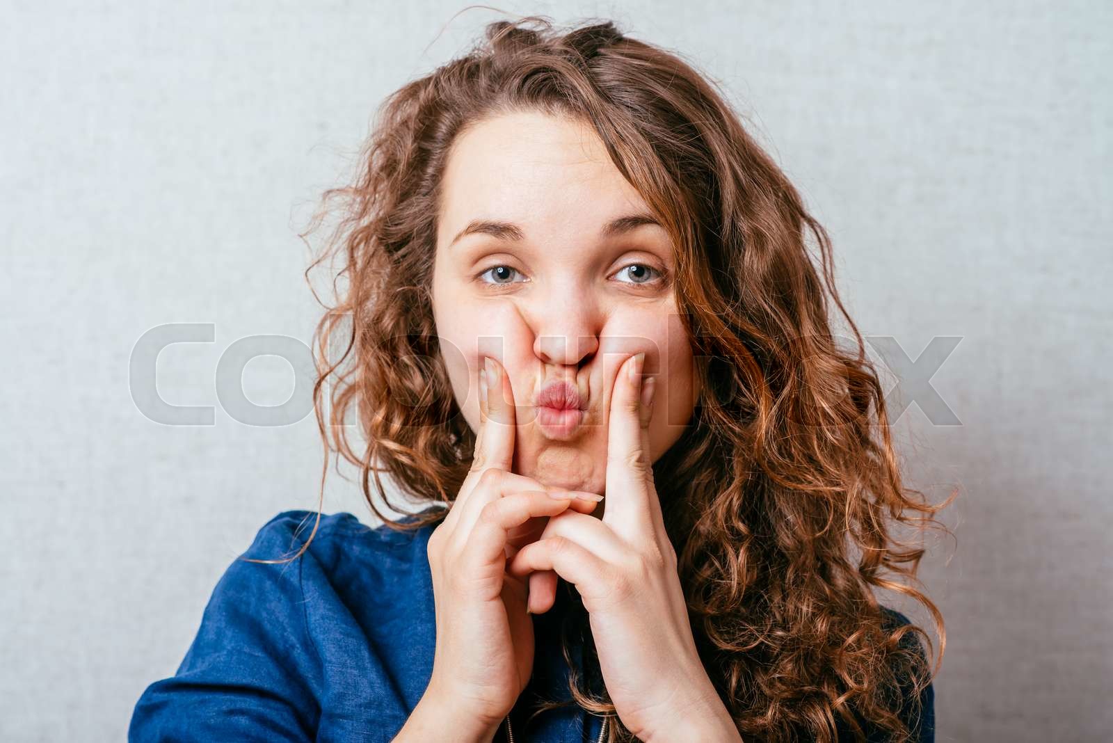Young woman squeezing her cheeks with her hands | Stock image | Colourbox