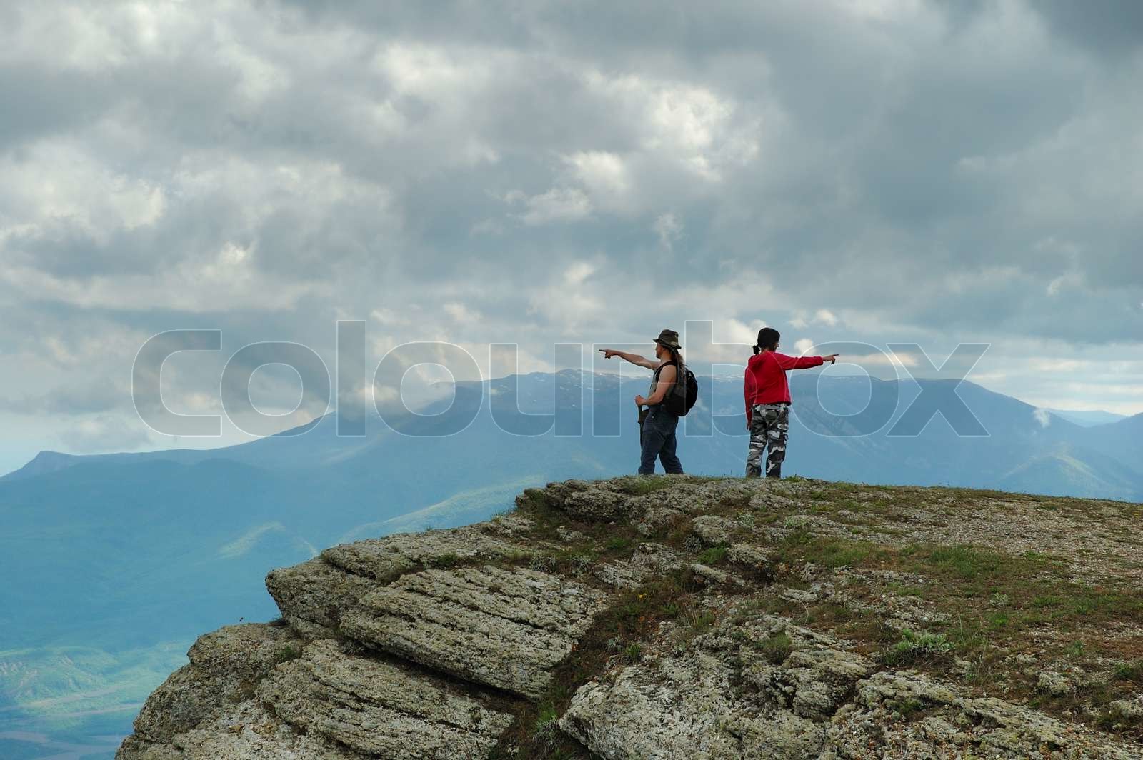 Two people on top of a mountain and pointing something in the distance ...