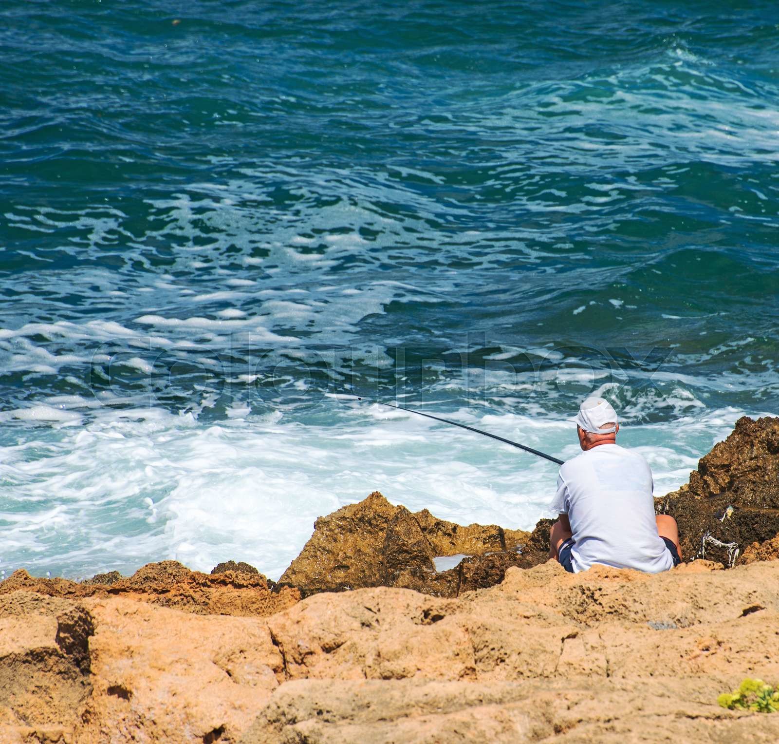 Man fishing on rocks by the sea. | Stock image | Colourbox