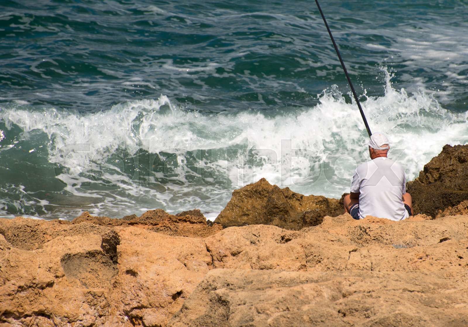 Man fishing on rocks by the sea. | Stock image | Colourbox