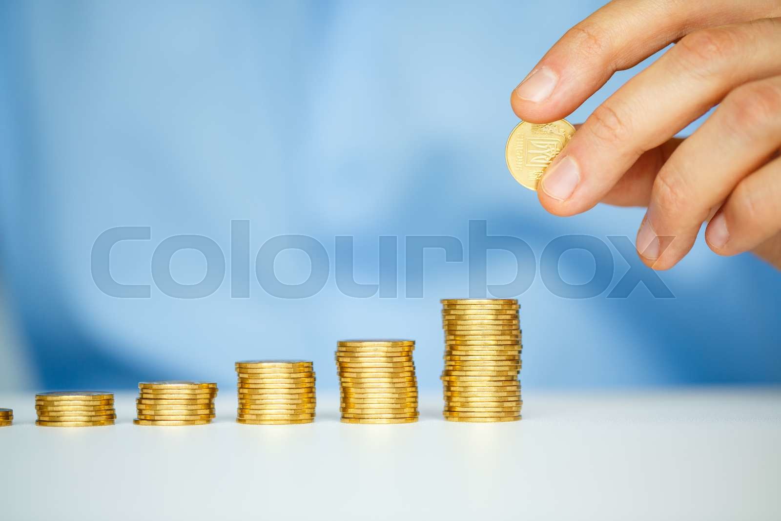 Male hand stacking gold coins into increasing columns | Stock image ...