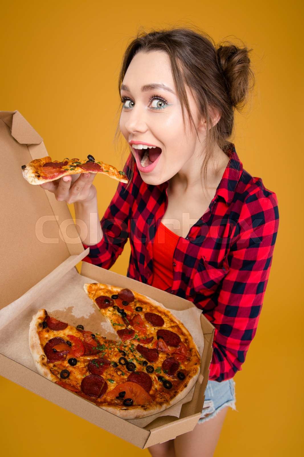 Joyful charming young woman standing and tasting pizza | Stock image ...