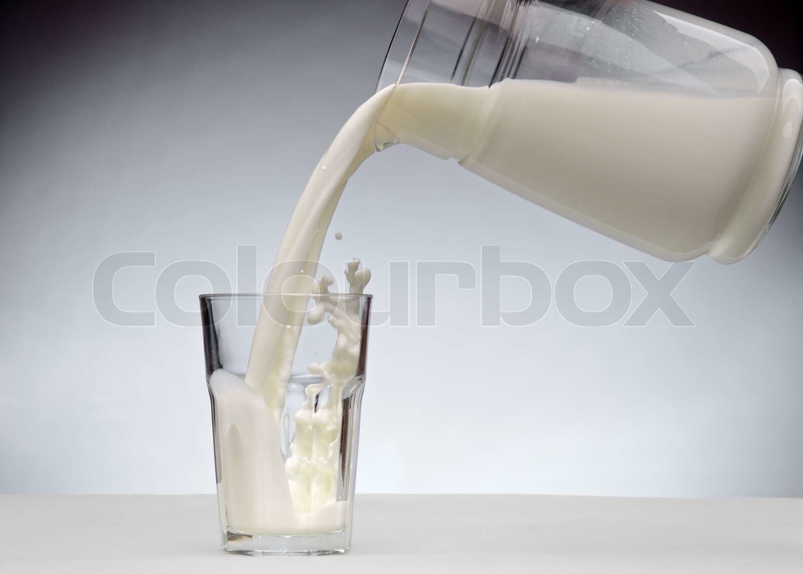Pouring a glass of milk with splash from jug | Stock image | Colourbox