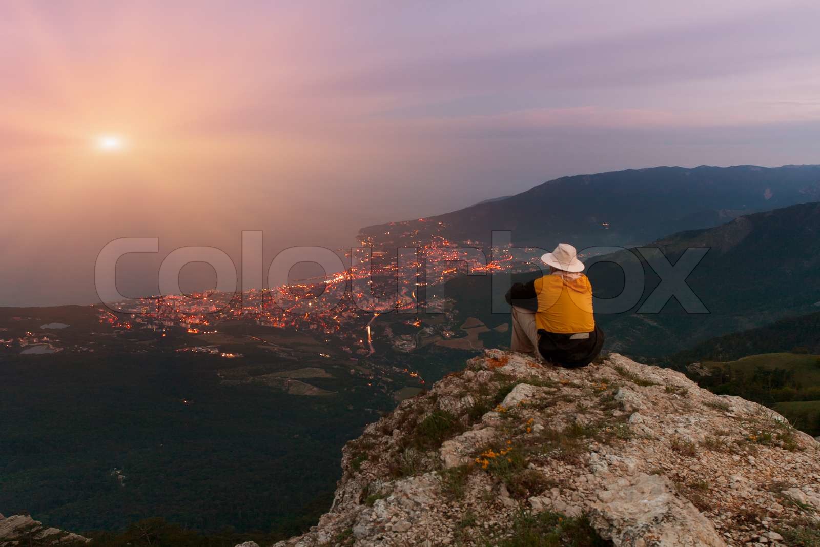 Man sitting on the edge of a cliff above the sea and looks at the ...