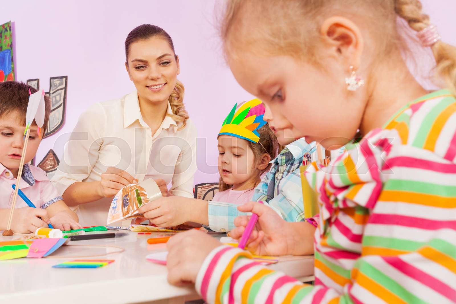 Teacher in kindergarten help kids make paper craft | Stock image ...