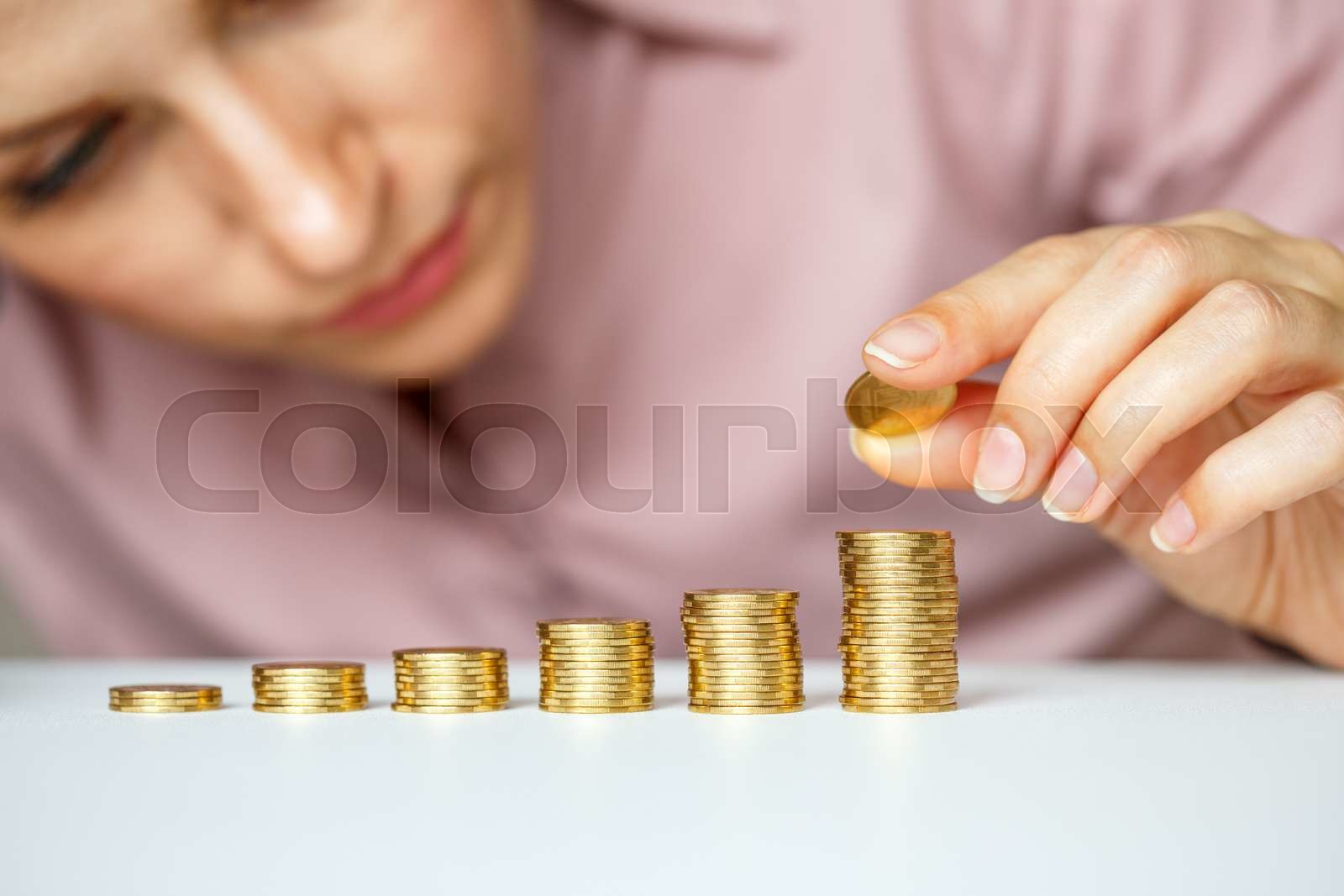 Woman stacking gold coins into increasing columns | Stock image | Colourbox