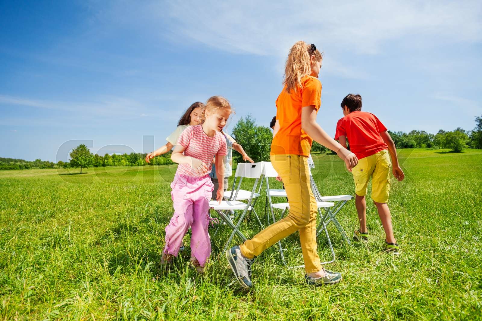 Children run around chairs playing a game outside | Stock image | Colourbox
