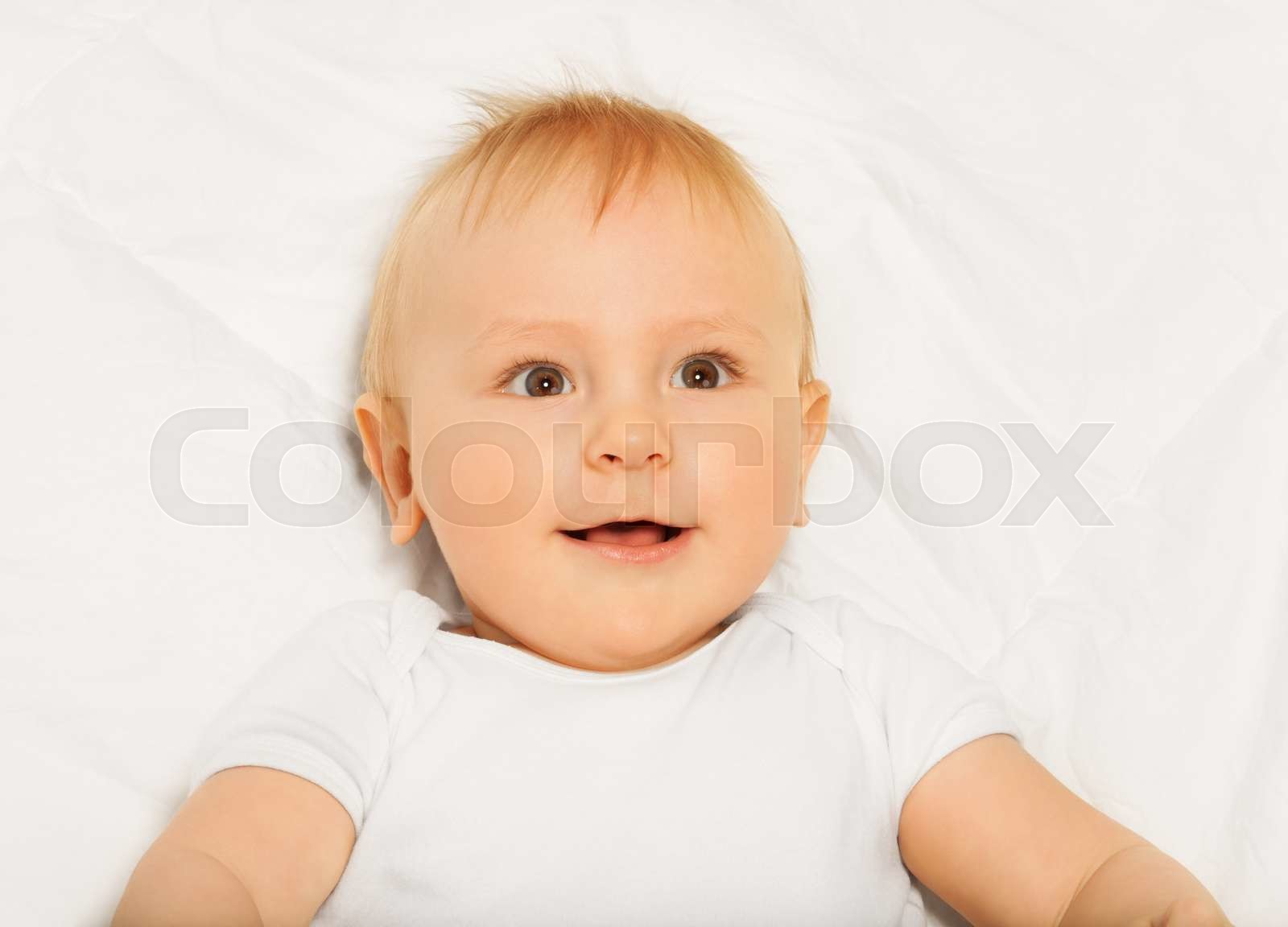 Amazed face of small baby wearing white babygro | Stock image | Colourbox