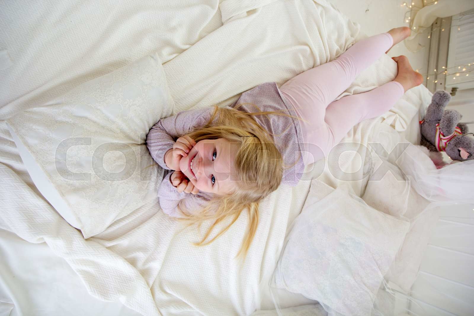 Happy child girl is lying down in the white bed | Stock image | Colourbox