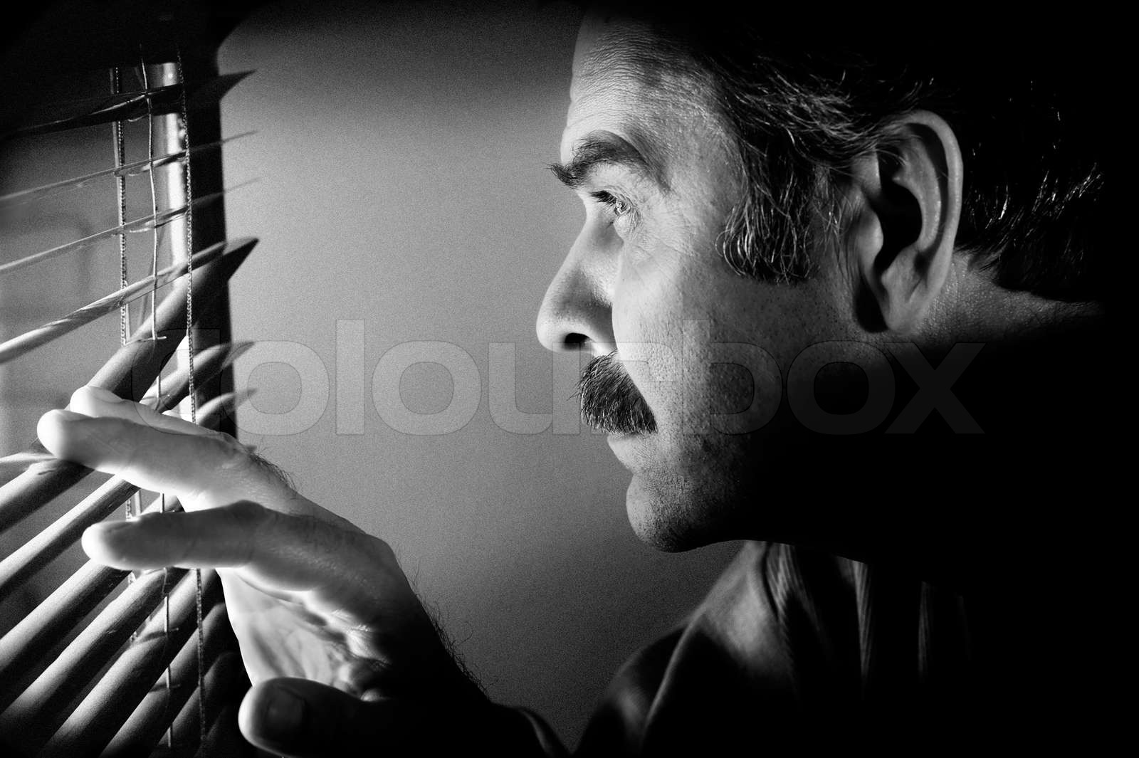 Low key concept photo of man looking furtively through window jalousies ...