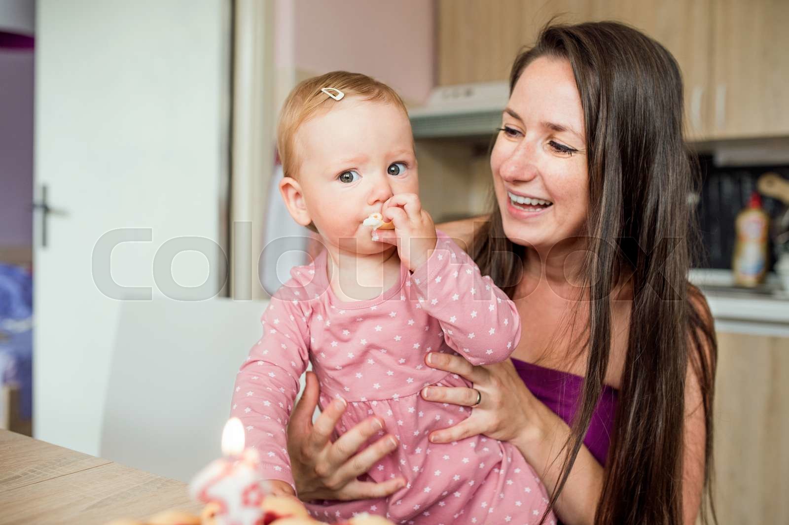 Mother holding her baby daughter eating birthday cake | Stock image ...