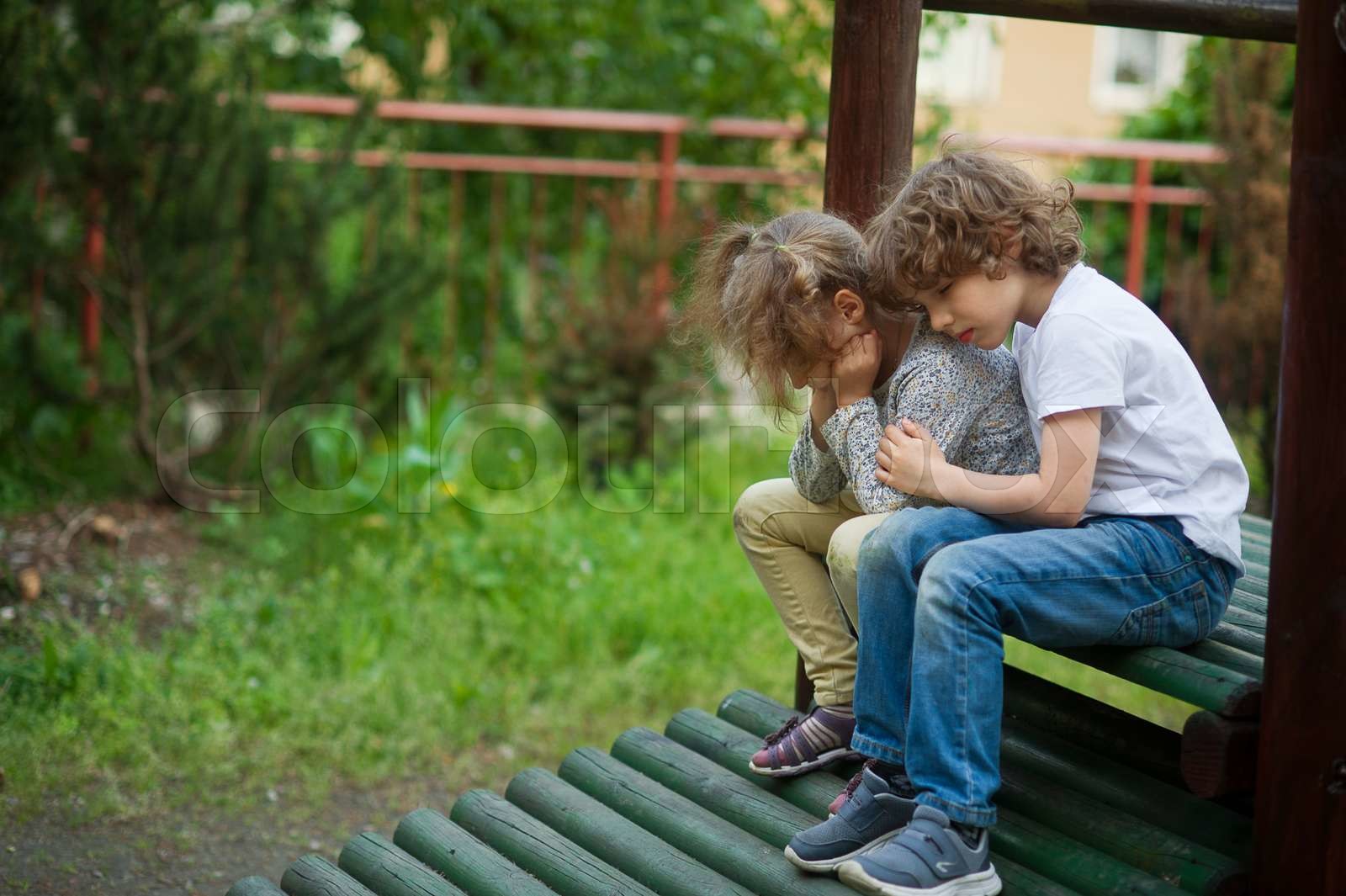 Two sad children sitting on a bench in the yard | Stock image | Colourbox