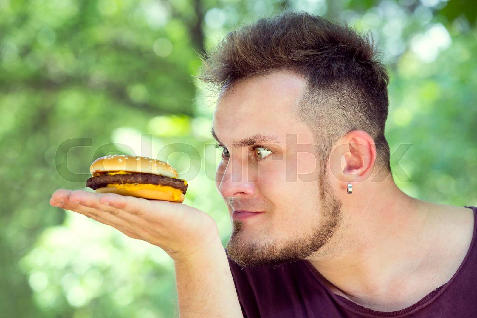 emotional young guy eating a cheeseburger on the nature | Stock image ...