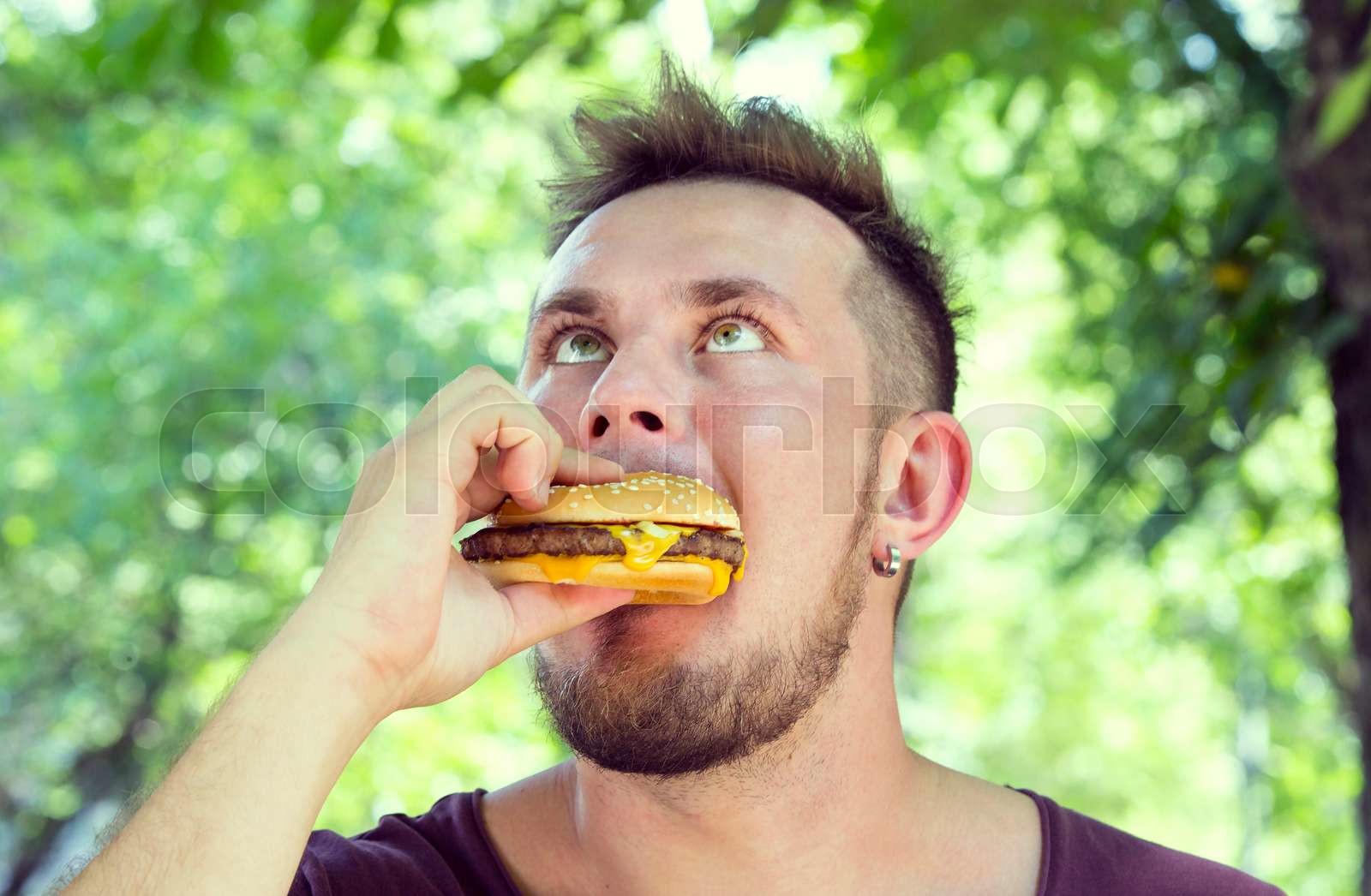 emotional young guy eating a cheeseburger on the nature | Stock image ...
