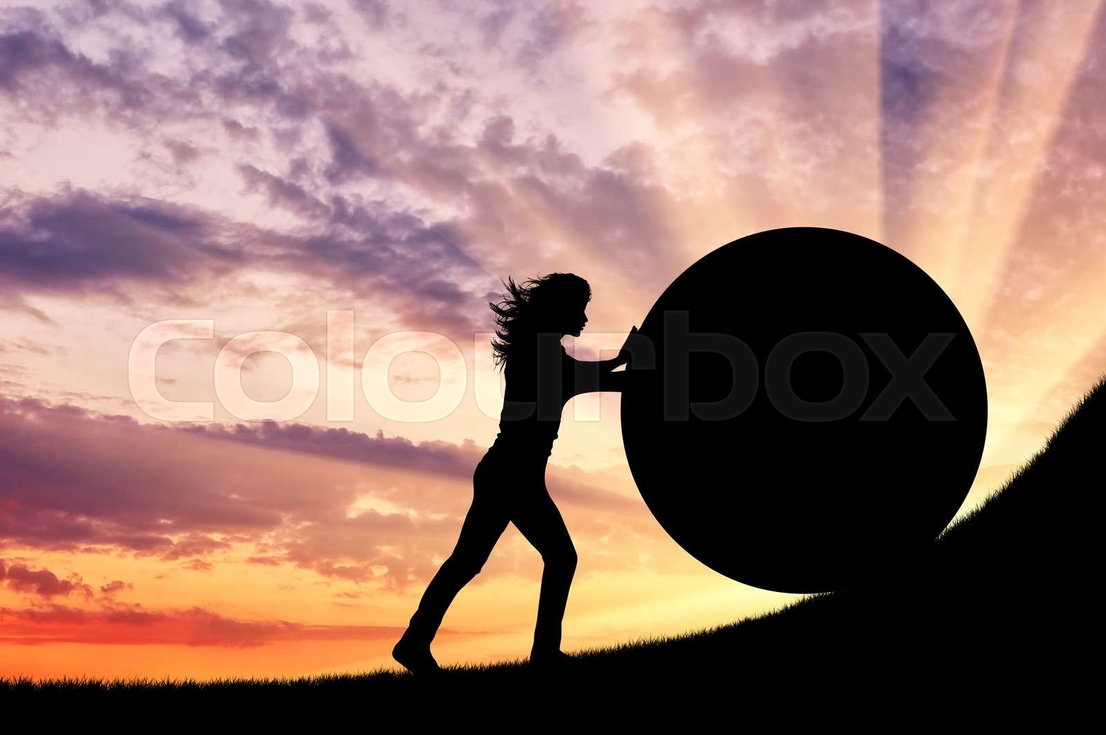 Silhouette of a strong woman pushing a stone up. | Stock image | Colourbox
