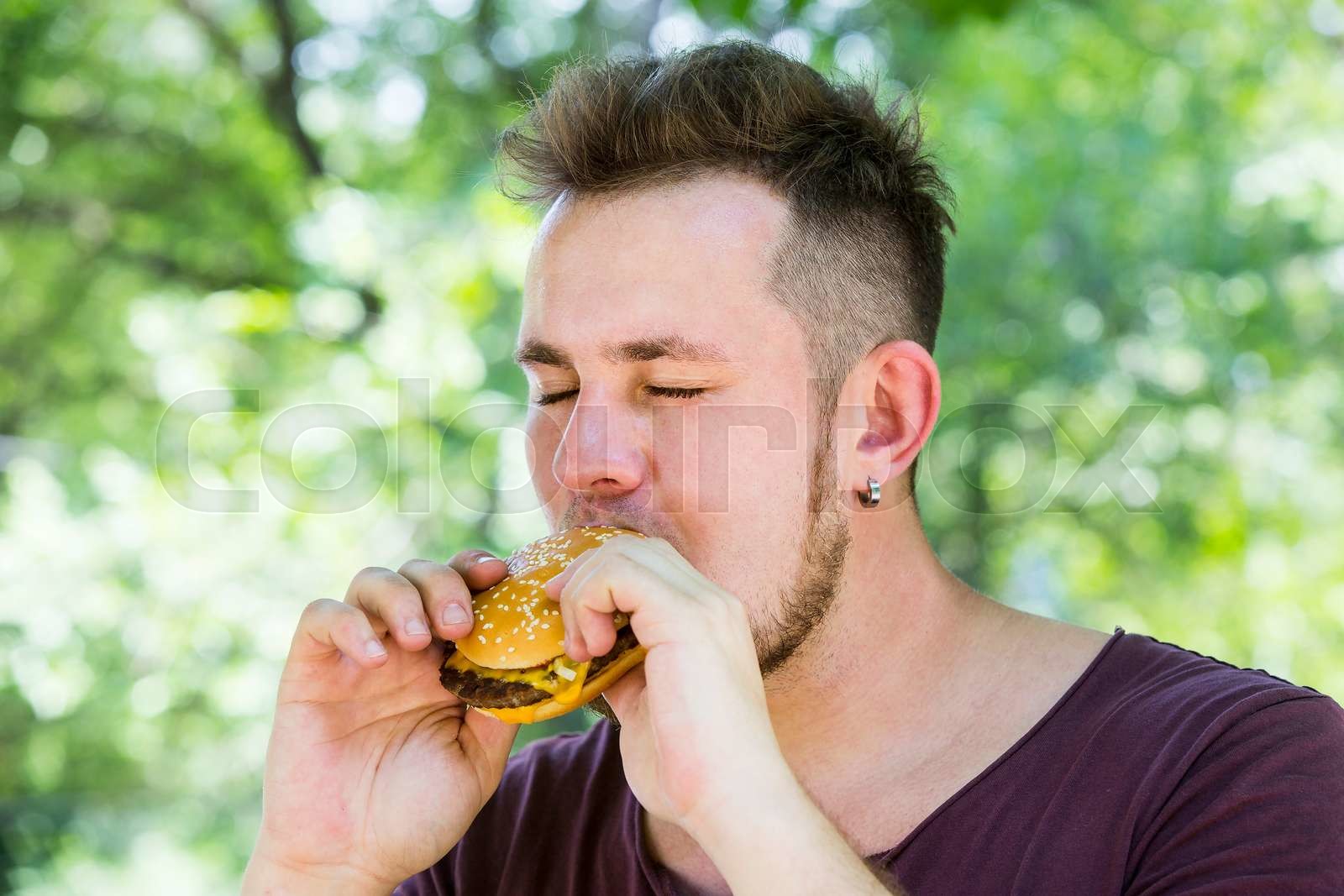 emotional young guy eating a cheeseburger on the nature | Stock image ...