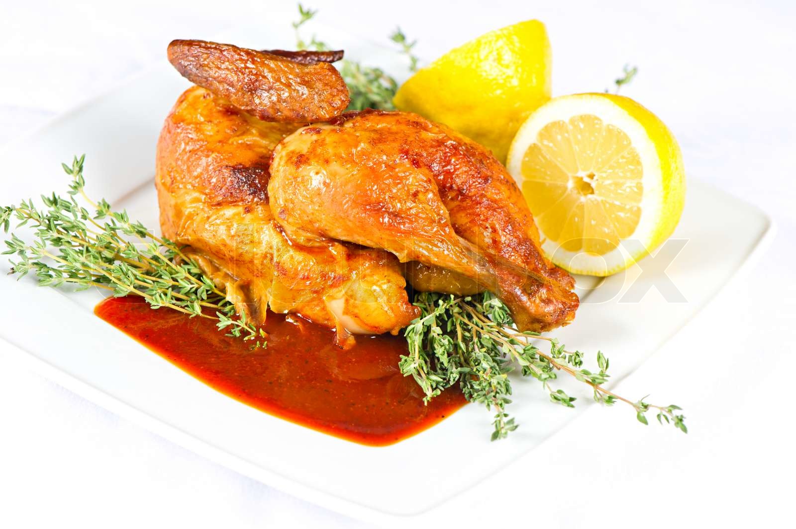 Gegrilltes Huhn auf einer weißen Platte mit pikanter Sauce und Zitrone ...
