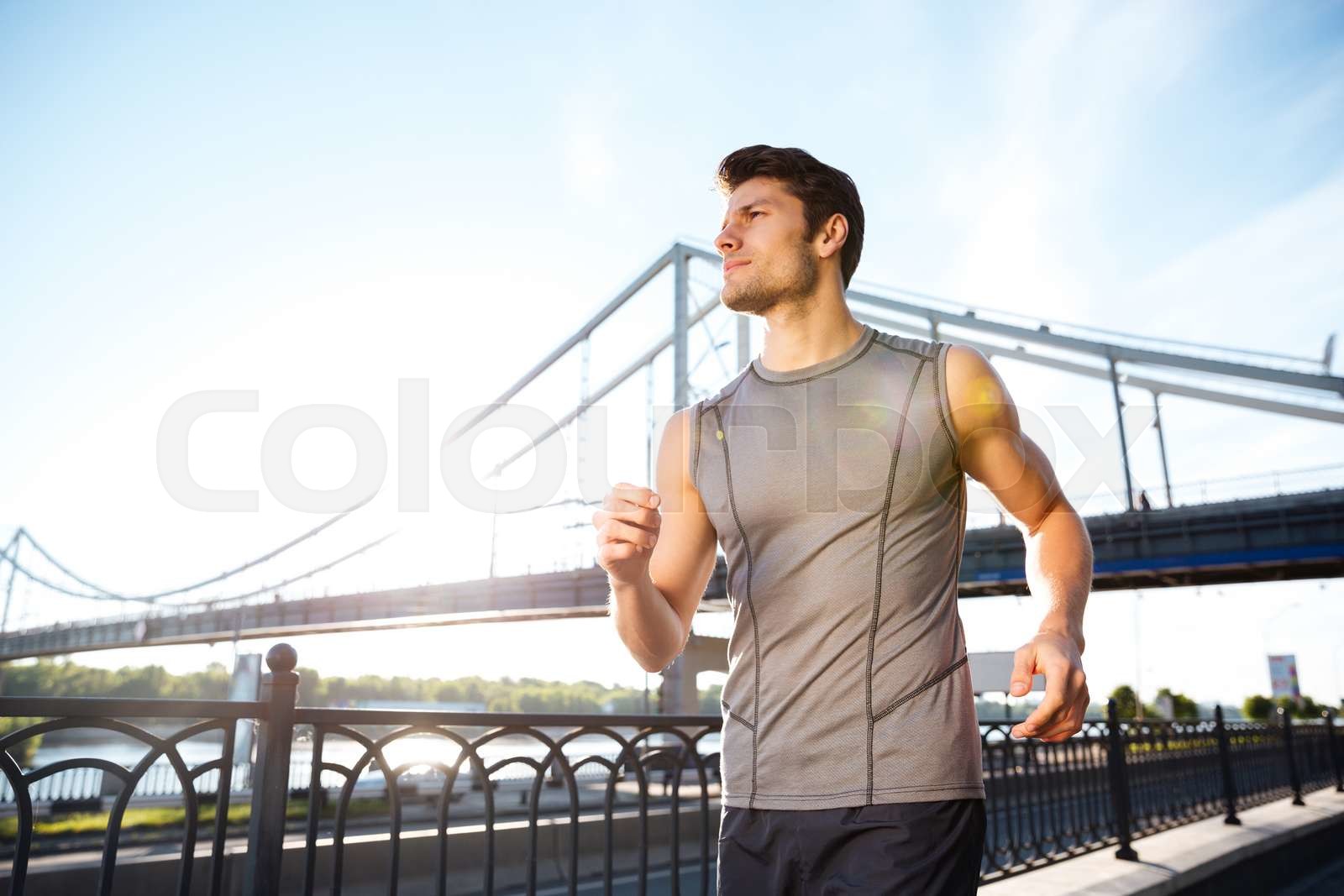 Handsome sports man running along modern bridge at sunset light | Stock ...