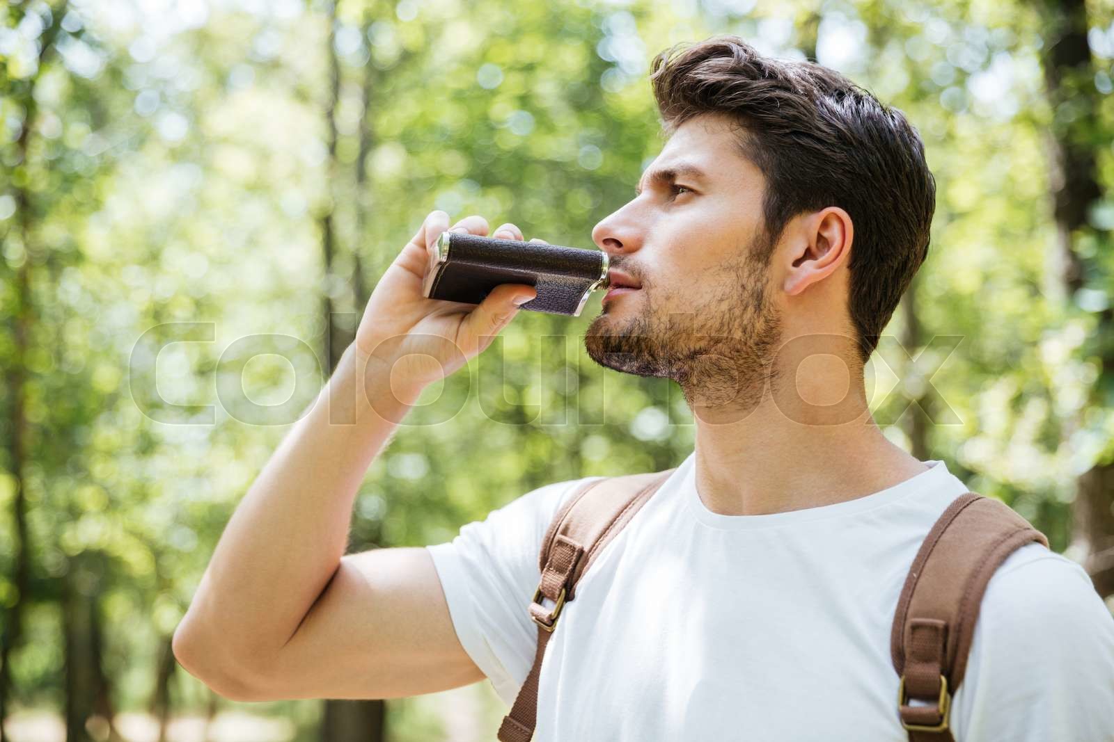 Man with backpack standing and drinking from flask in forest | Stock ...