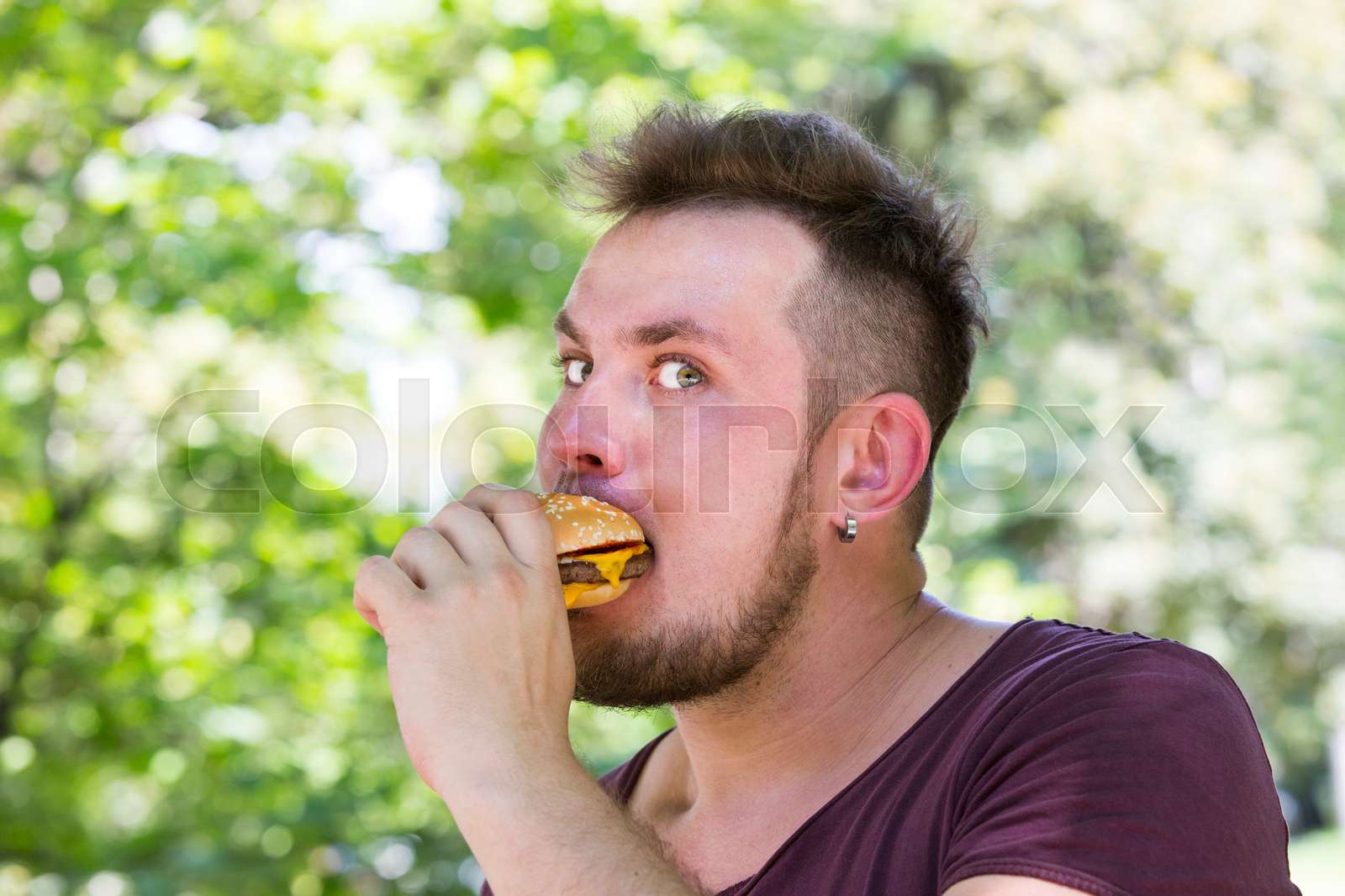 emotional young guy eating a cheeseburger on the nature | Stock image ...