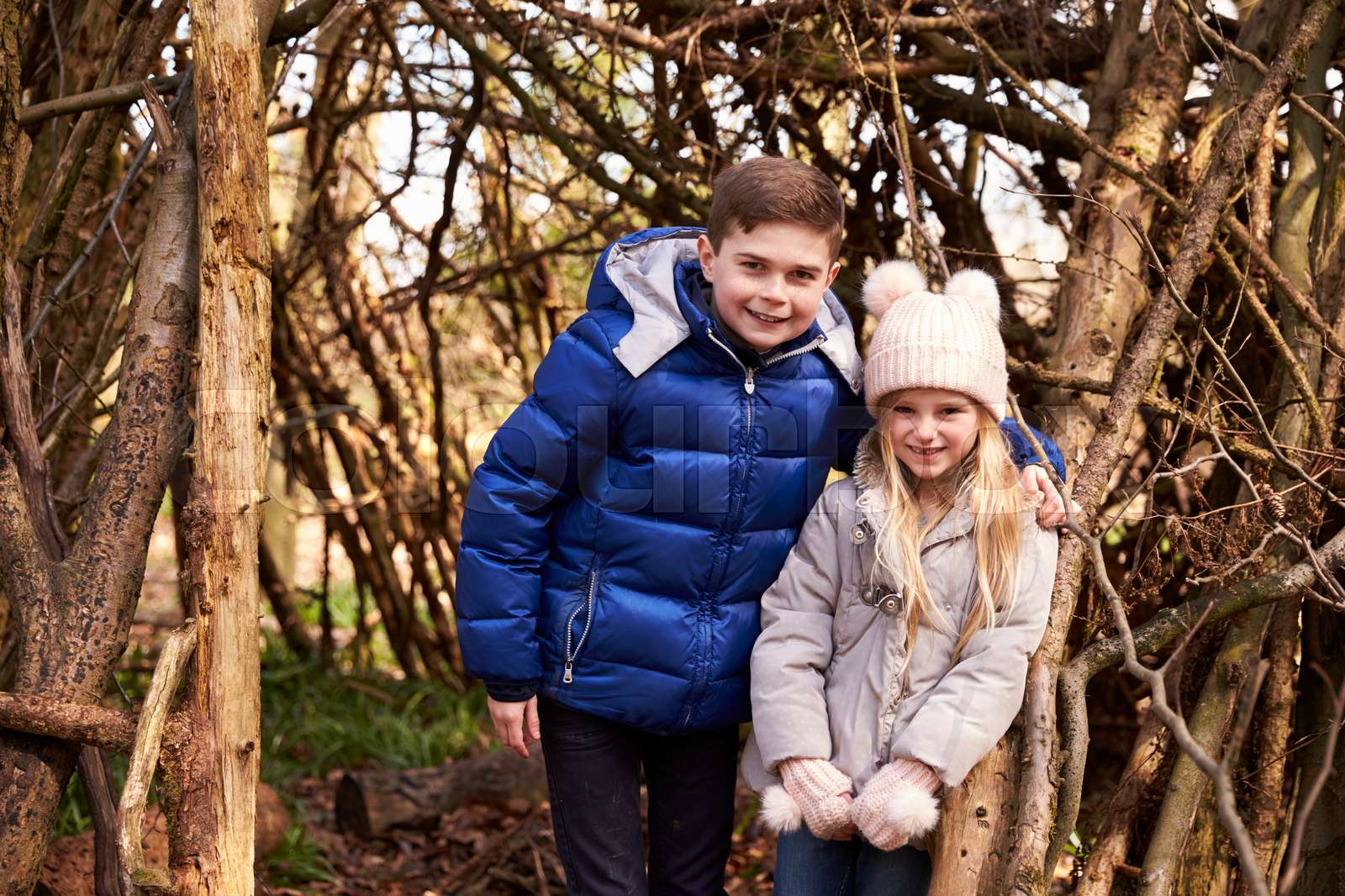 Brother and sister under shelter of branches look to camera | Stock ...