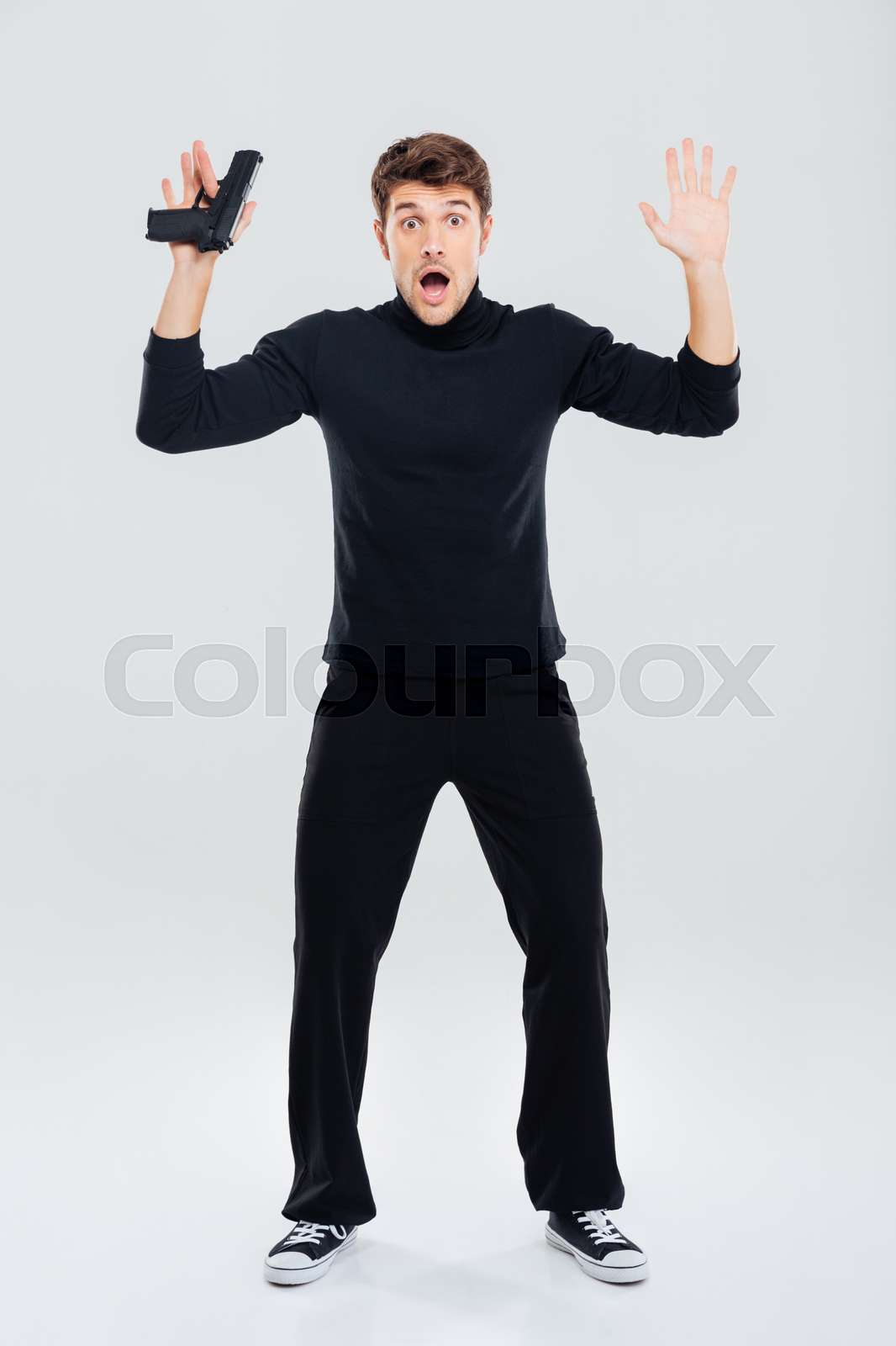 Scared young man holding gun and standing with hands up | Stock image ...