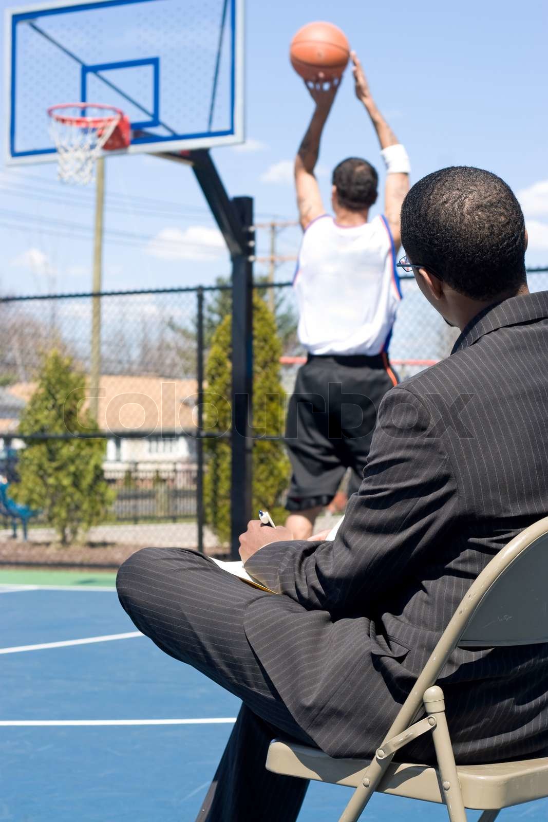 A basketball coach in a business suit observing a player on the team ...