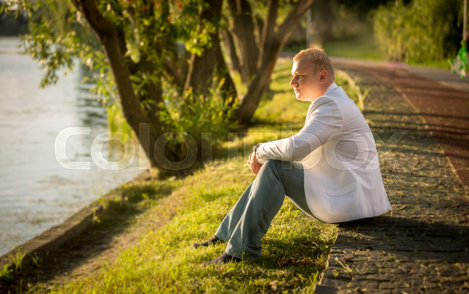 Toned image of stylish man siting on ground at park and looking at ...