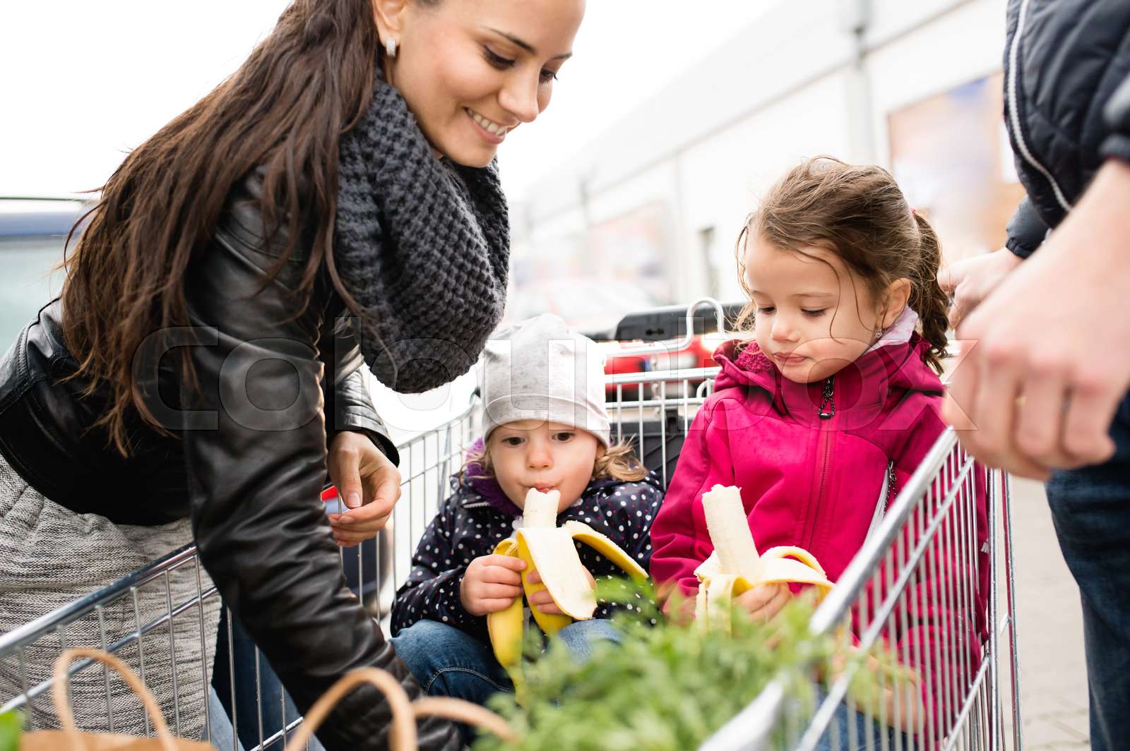 Parents pushing shopping cart with groceries and their daughters ...